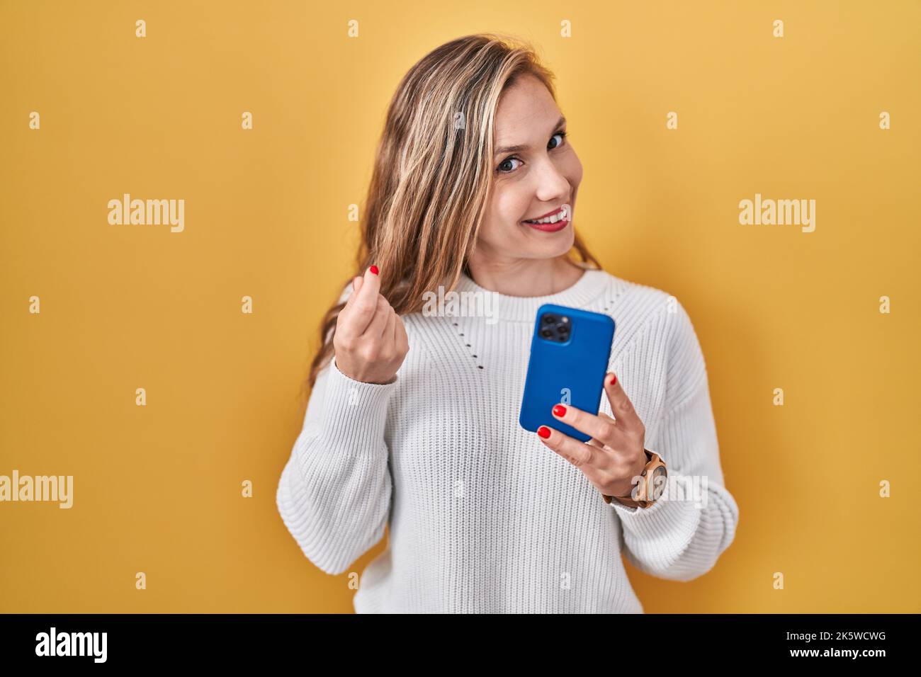 Young blonde woman using smartphone typing message doing money gesture ...