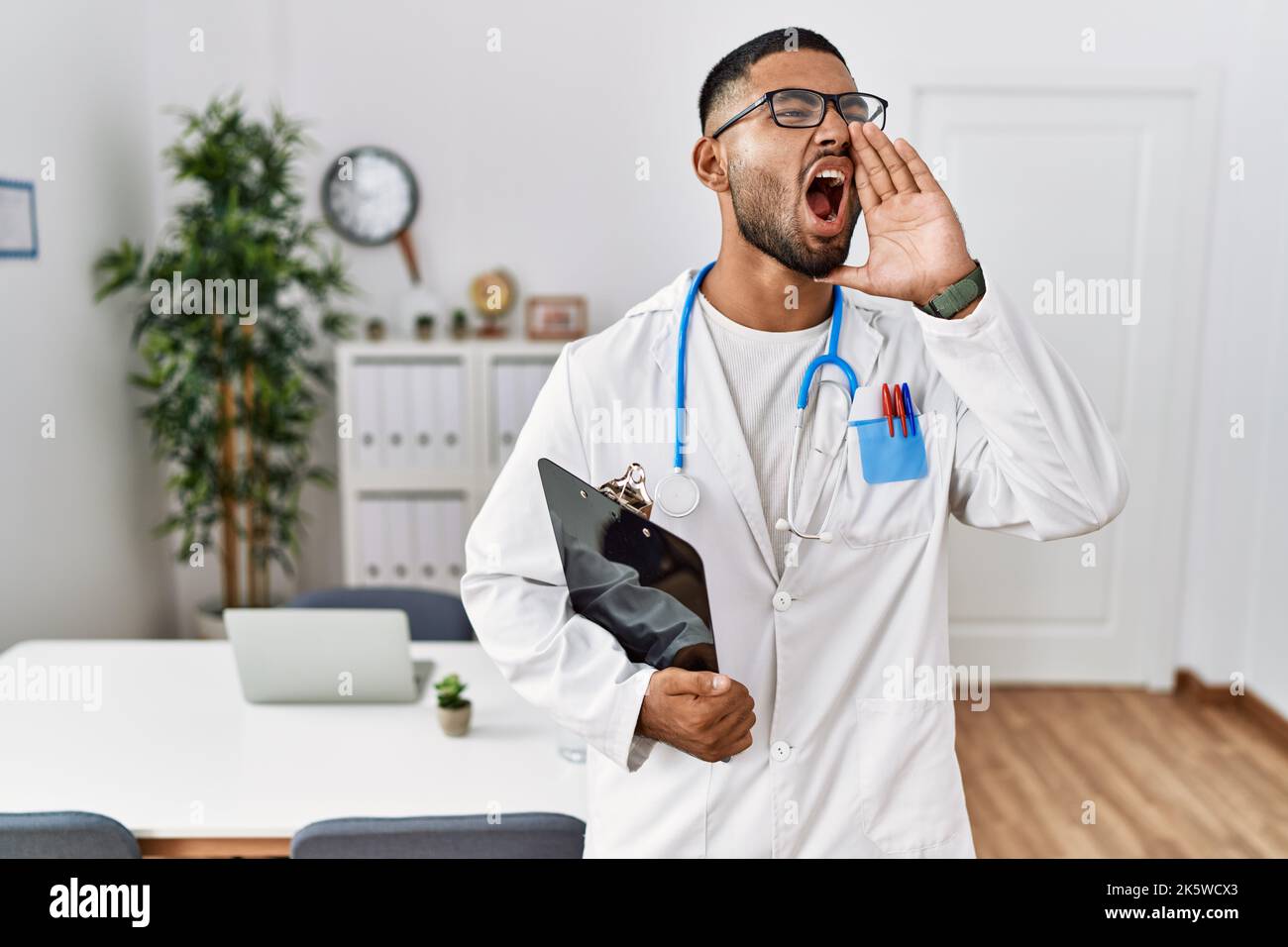 Young indian man wearing doctor uniform and stethoscope shouting and ...