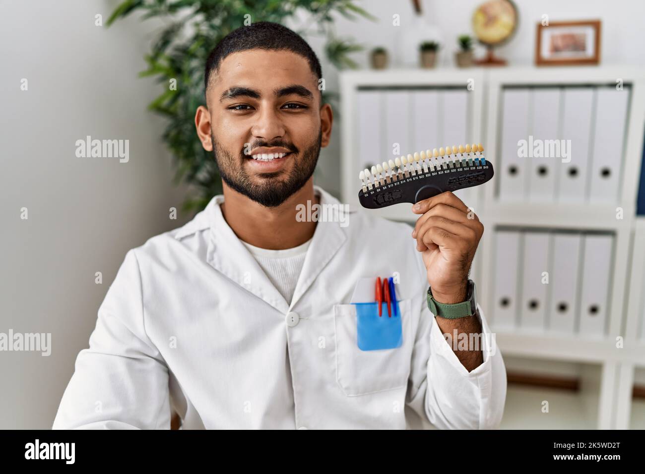 Young indian man holding teeth whitening palette looking positive and ...