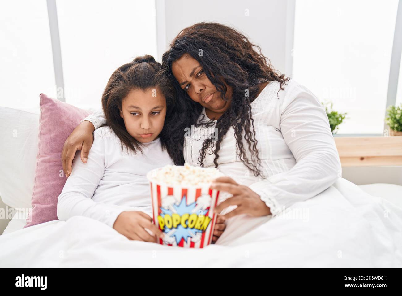 Mother and young daughter eating popcorn in the bed depressed and worry ...