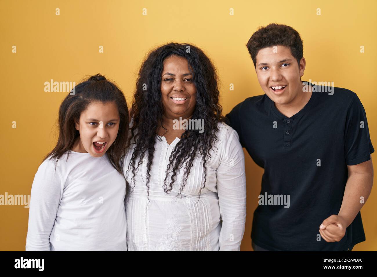 Family of mother, daughter and son standing over yellow background ...