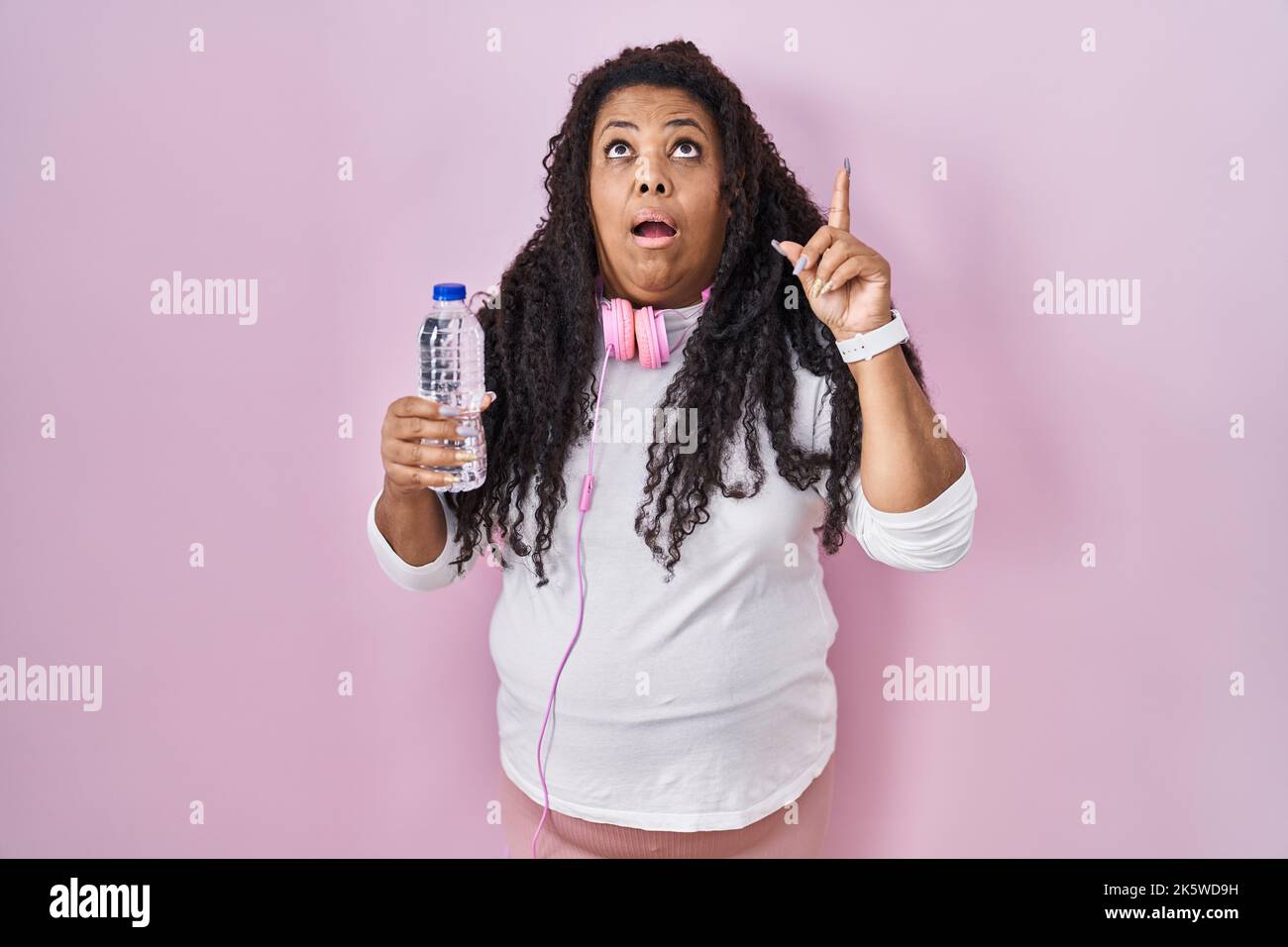 Plus size hispanic woman wearing sportswear and headphones amazed and ...