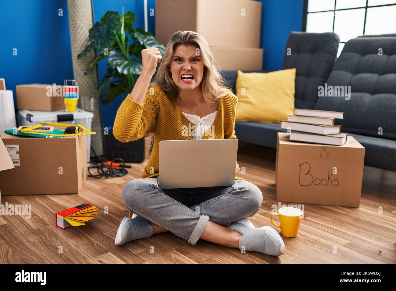 Young woman sitting on the floor at new home using laptop angry and mad ...