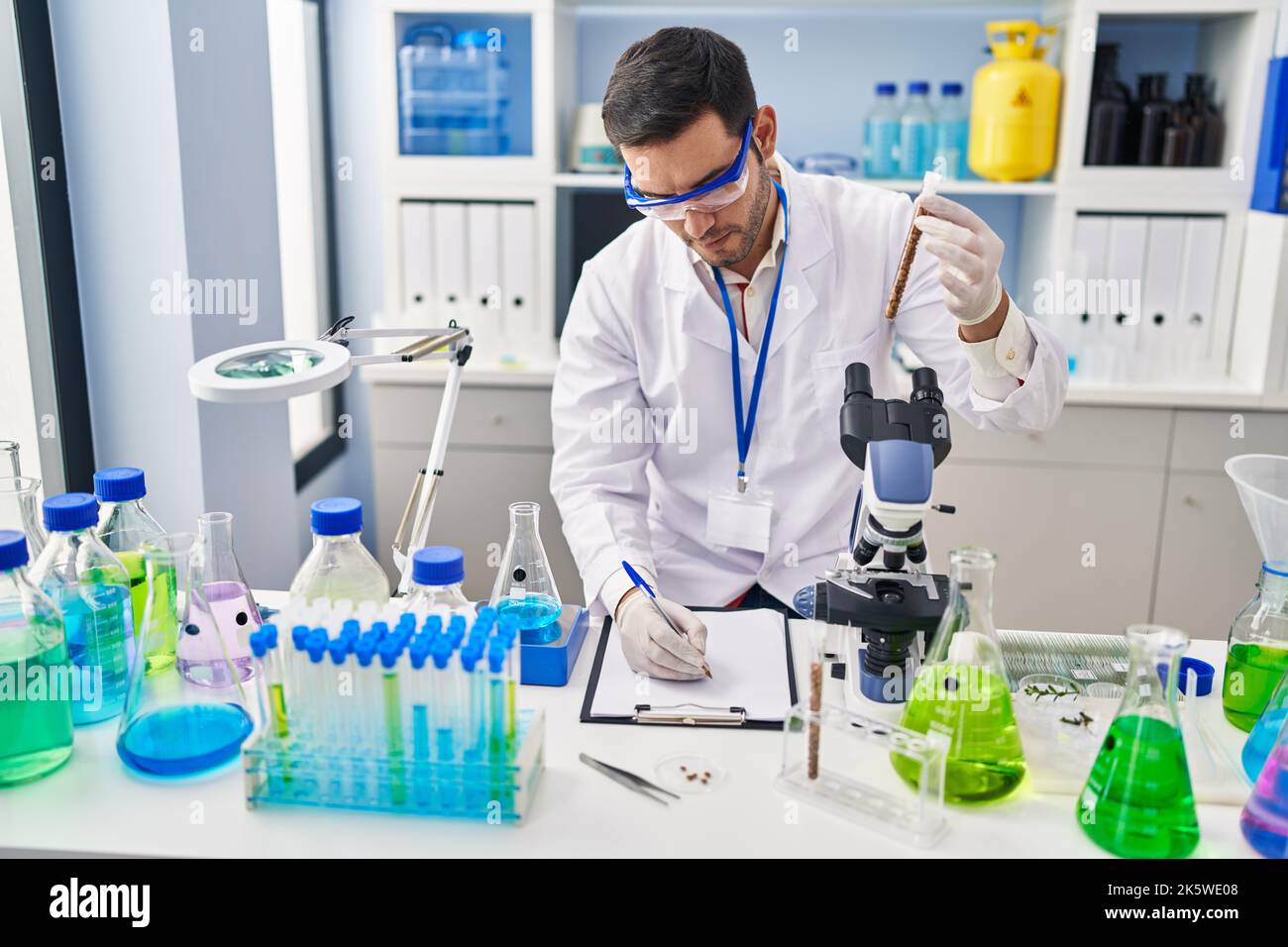 Young hispanic man scientist holding test tube writing report at ...