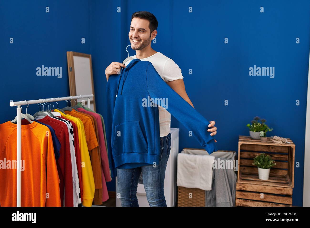 Young hispanic man putting clothes on clothes rack at laundry room ...