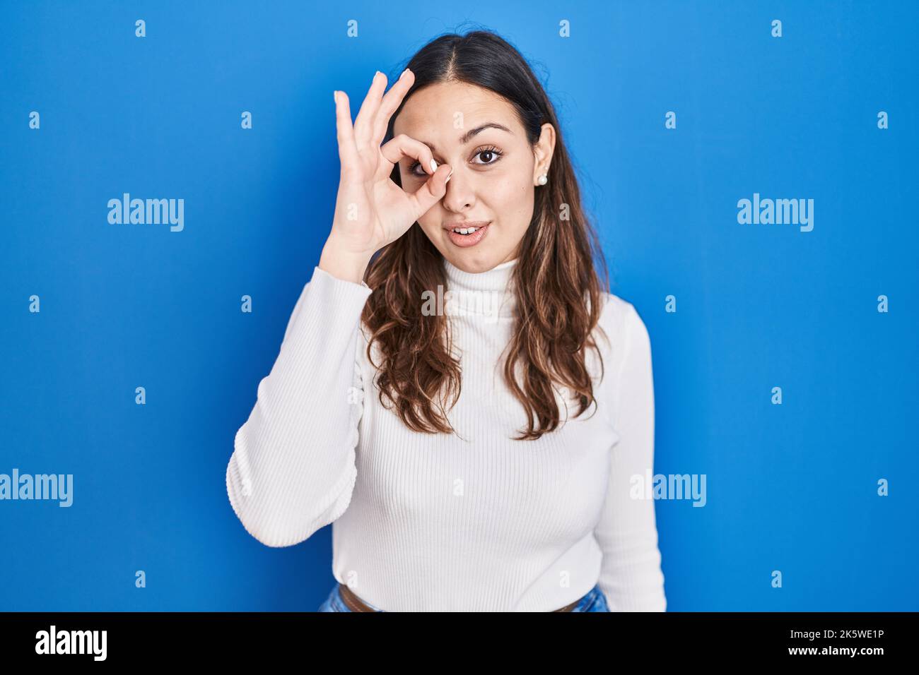 Young hispanic woman standing over blue background doing ok gesture ...