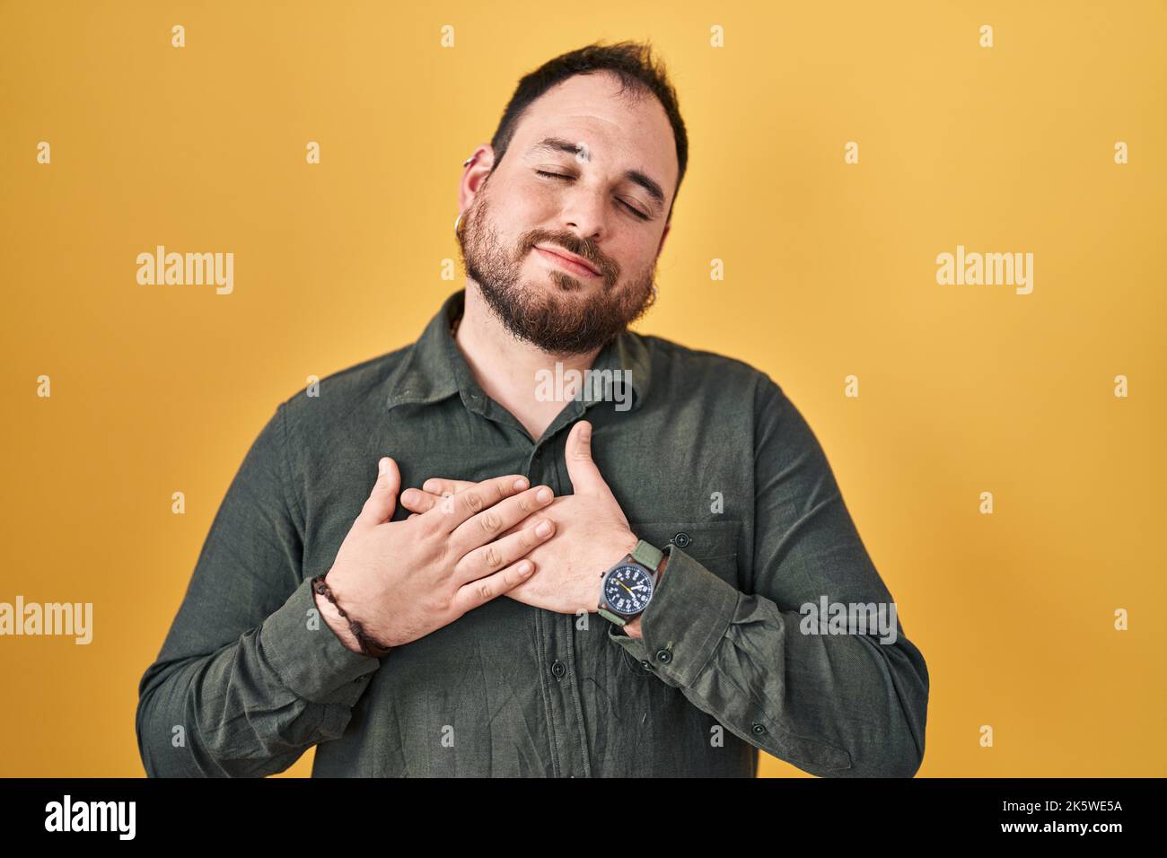 Plus size hispanic man with beard standing over yellow background ...
