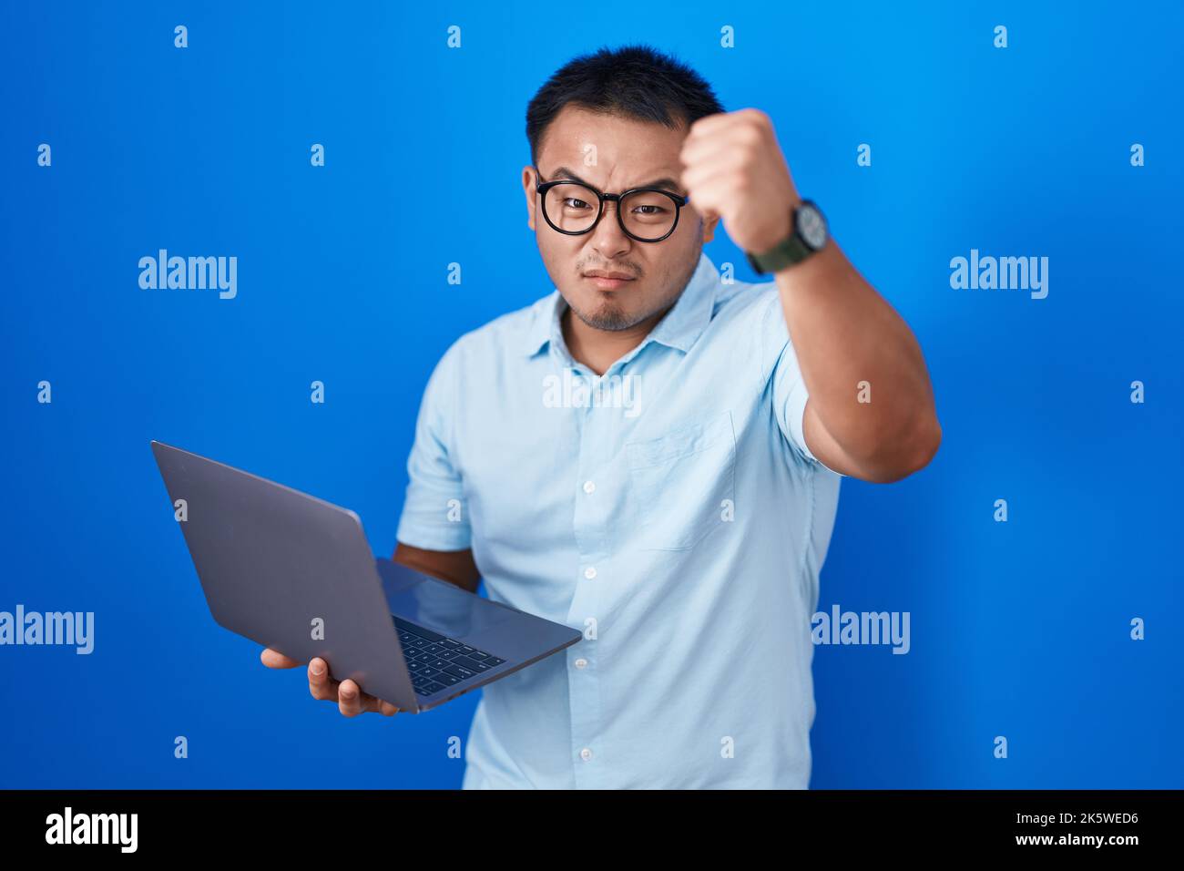 Chinese young man using computer laptop angry and mad raising fist ...