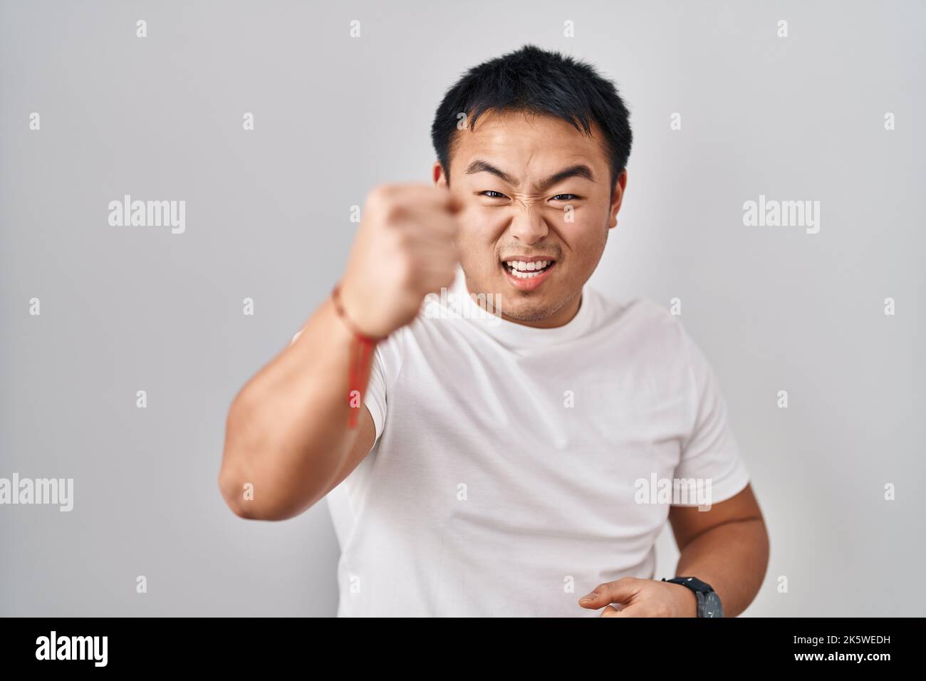 Young chinese man standing over white background angry and mad raising ...