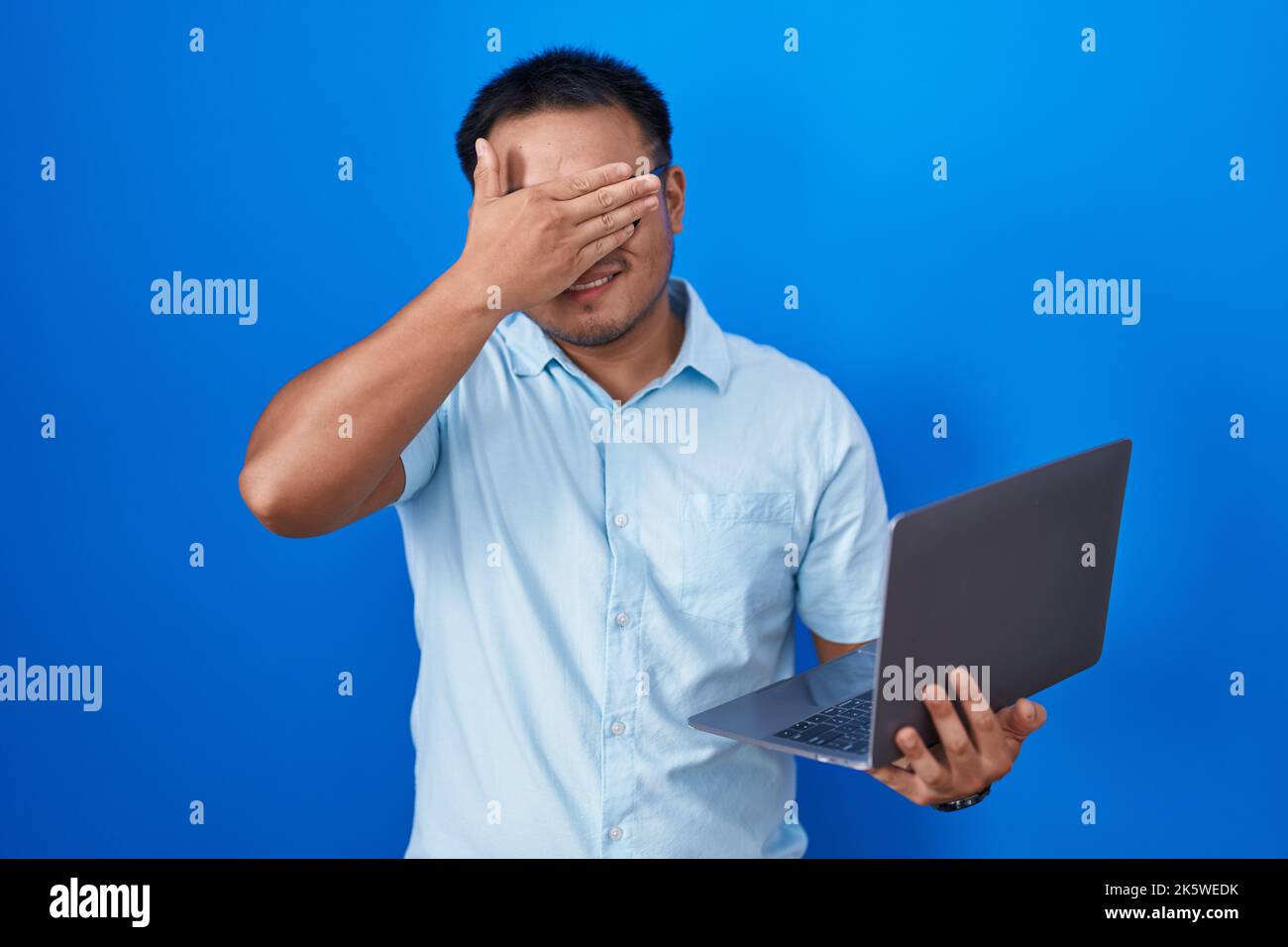 Chinese young man using computer laptop smiling and laughing with hand ... Chinese young man using computer laptop smiling and laughing with hand ...
