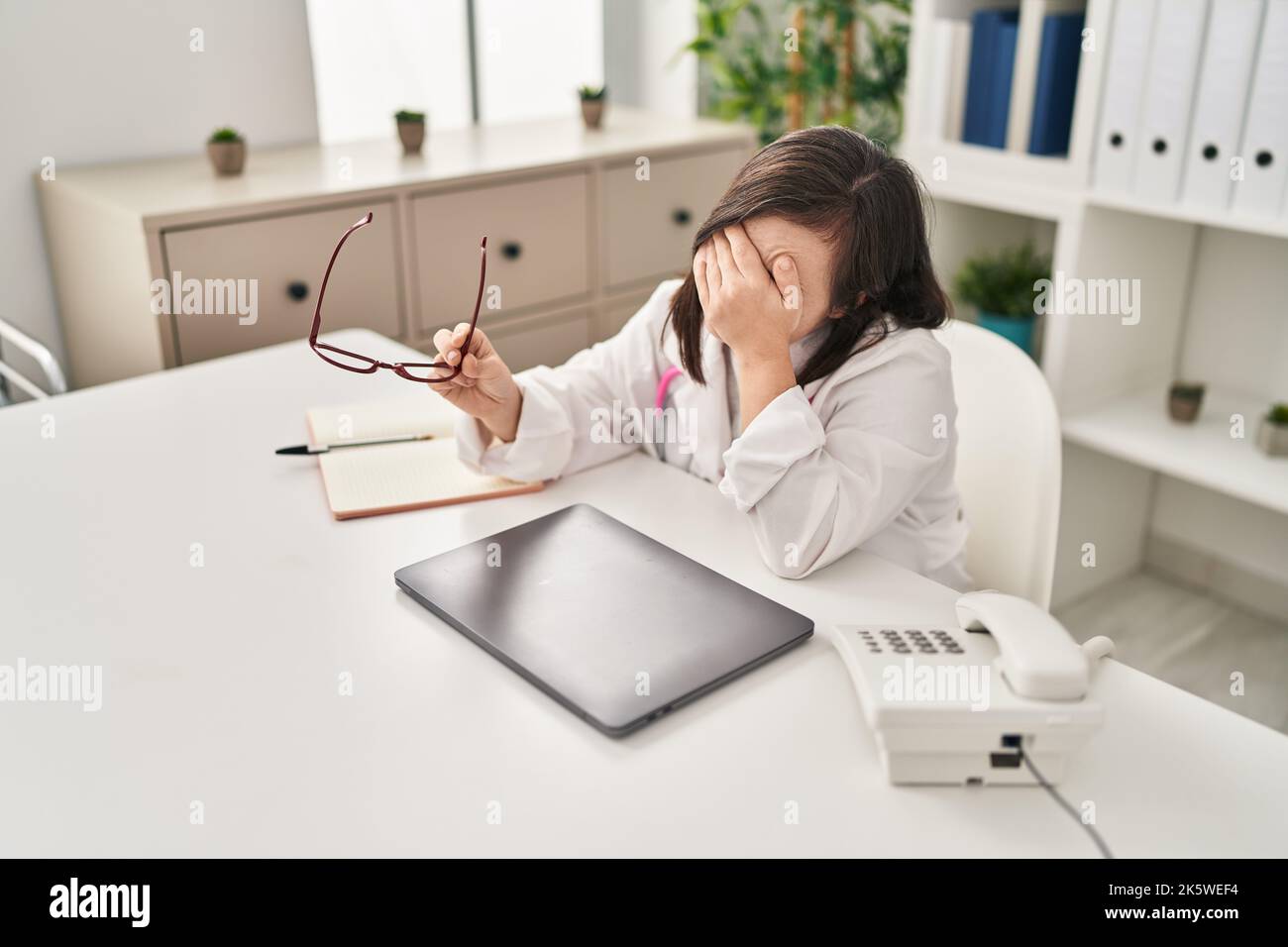 Down syndrome woman wearing doctor uniform stressed working at clinic ...