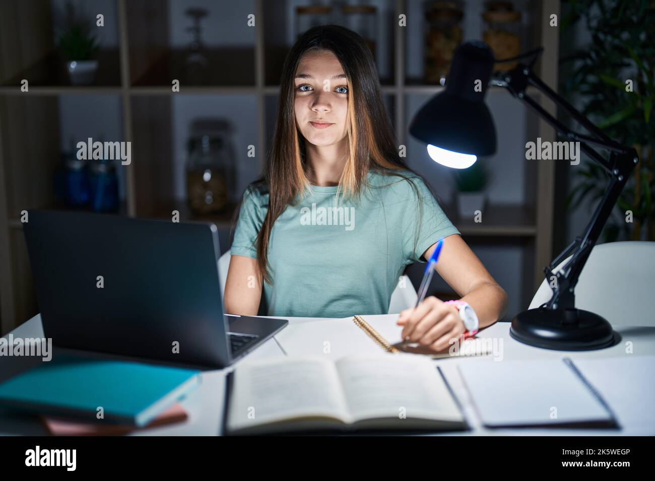 Teenager girl doing homework at home late at night looking to side ...