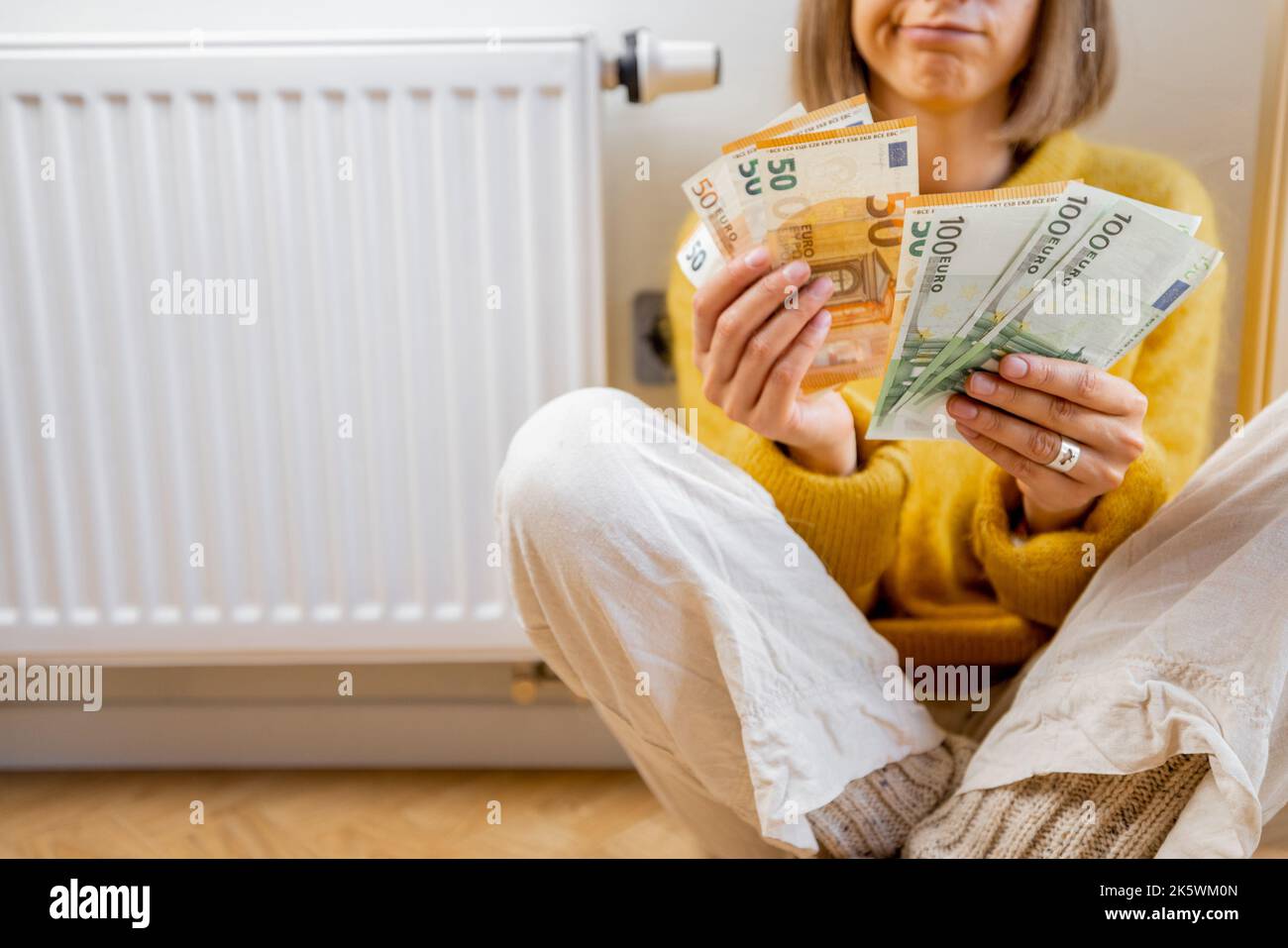 Warmly dressed woman counting money near radiator Stock Photo - Alamy