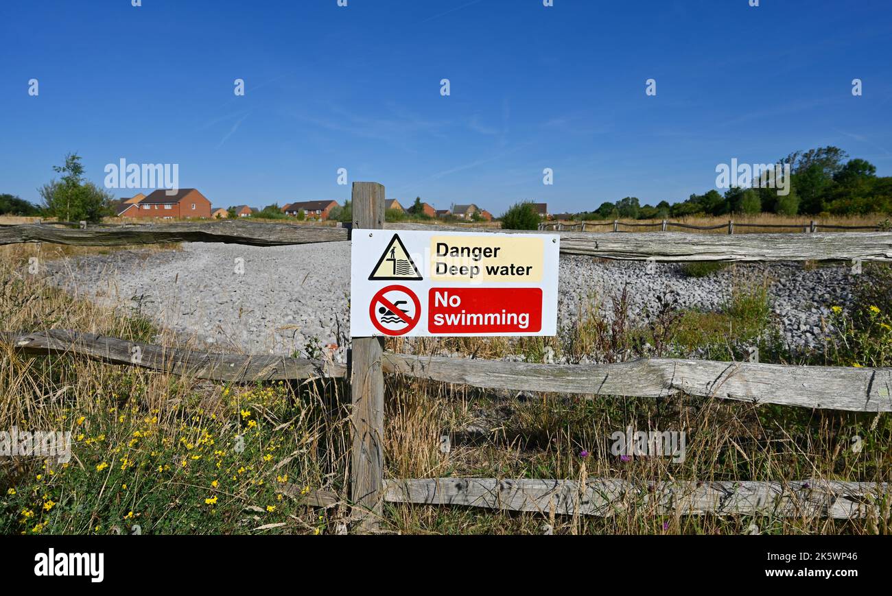 A dried up pond with "no swimming" and "danger" signs under the blue ...