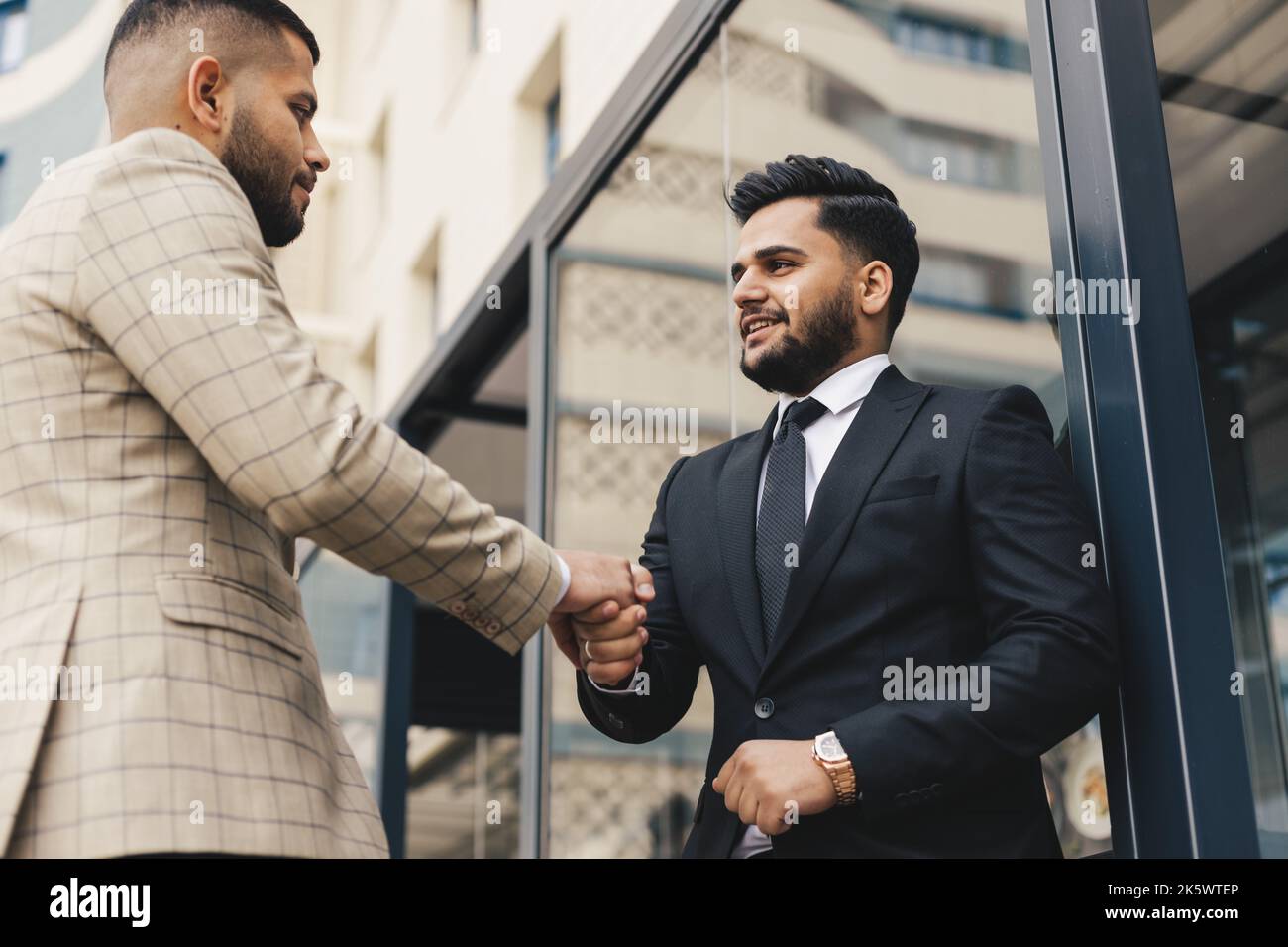 Business people outdoor meeting. Two men in suits hold out their hands ...