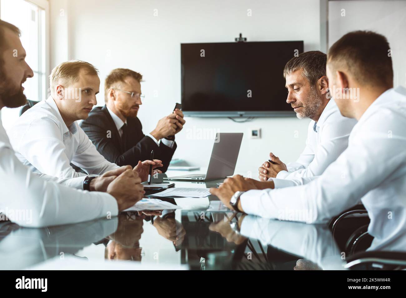 A group of company employees sits at a table in a meeting room. A team ...