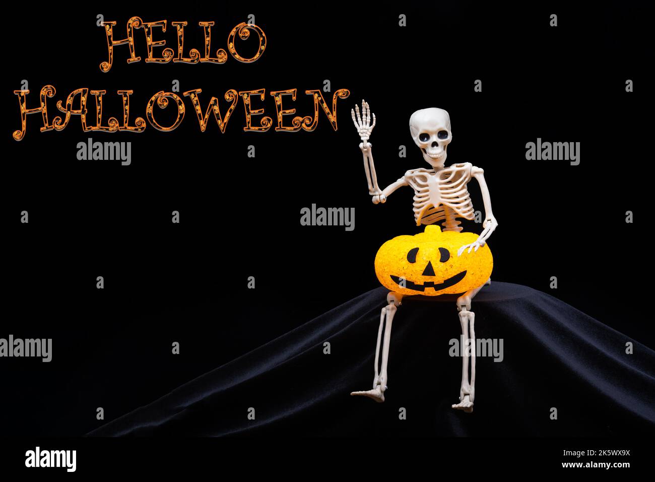 Greeting a human skeleton waving, holding an orange pumpkin on a black ...