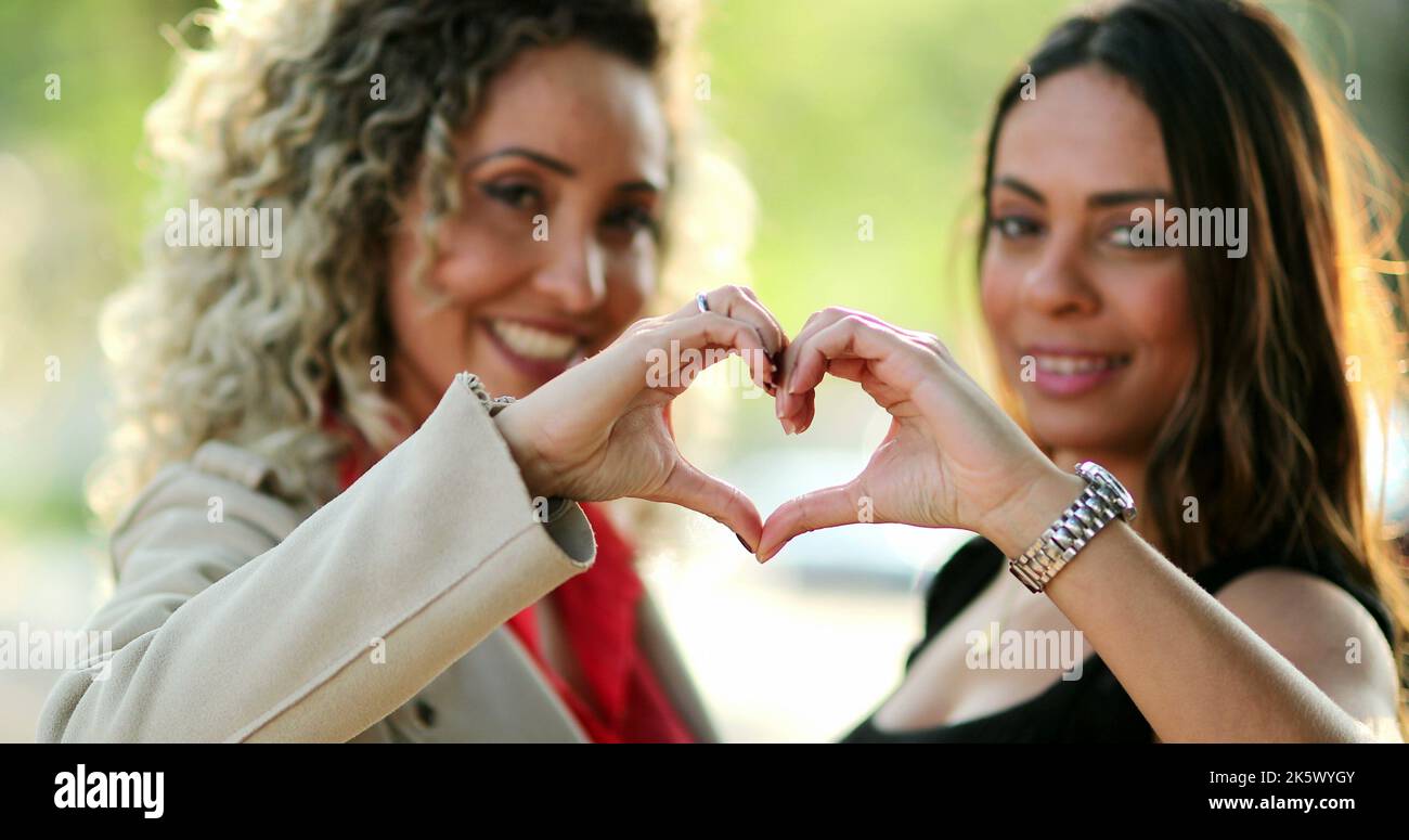 Two women doing heart symbol with hands outside Stock Photo - Alamy