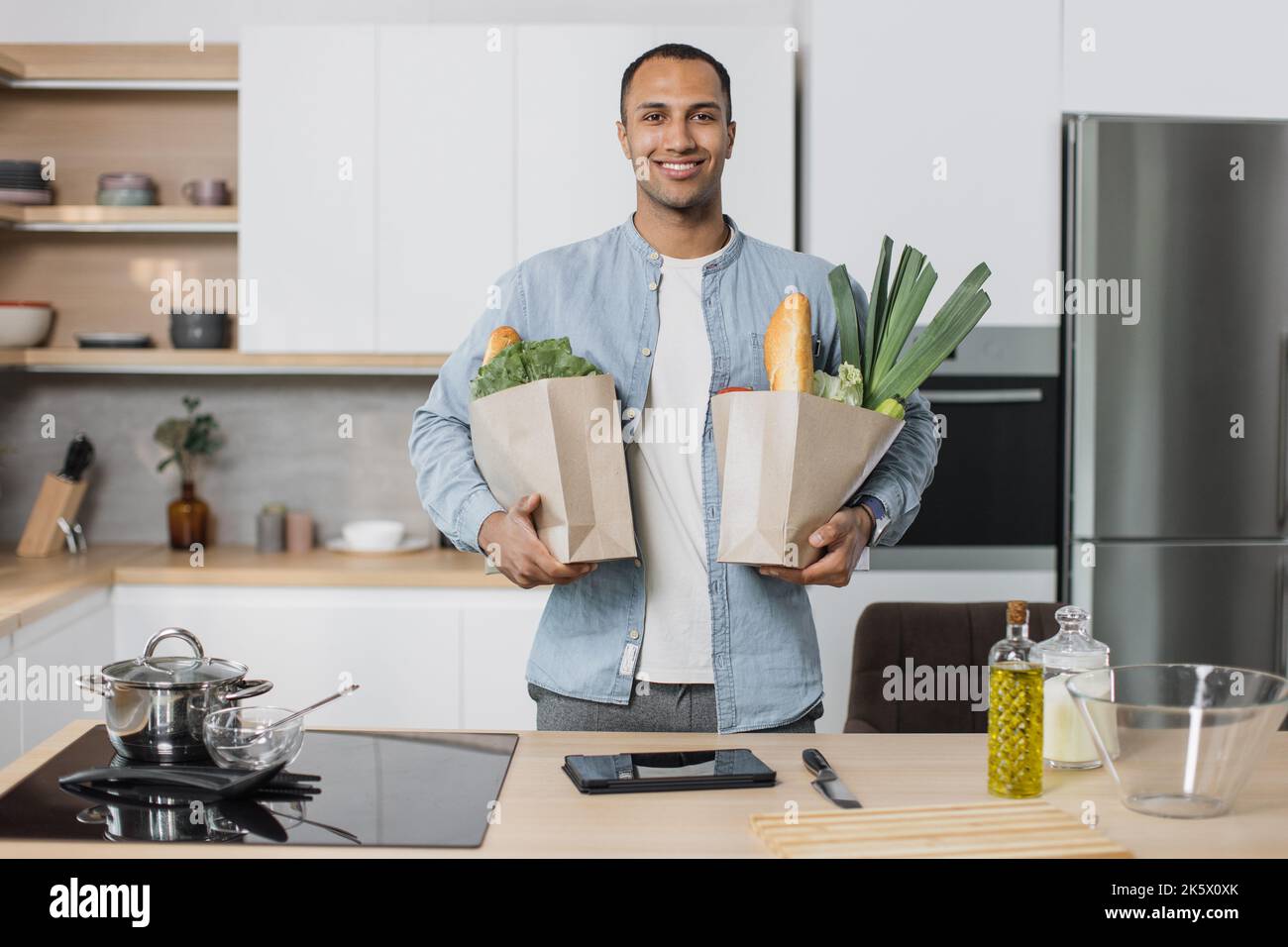 Young attractive indian man in kitchen holding two paper grocery ...
