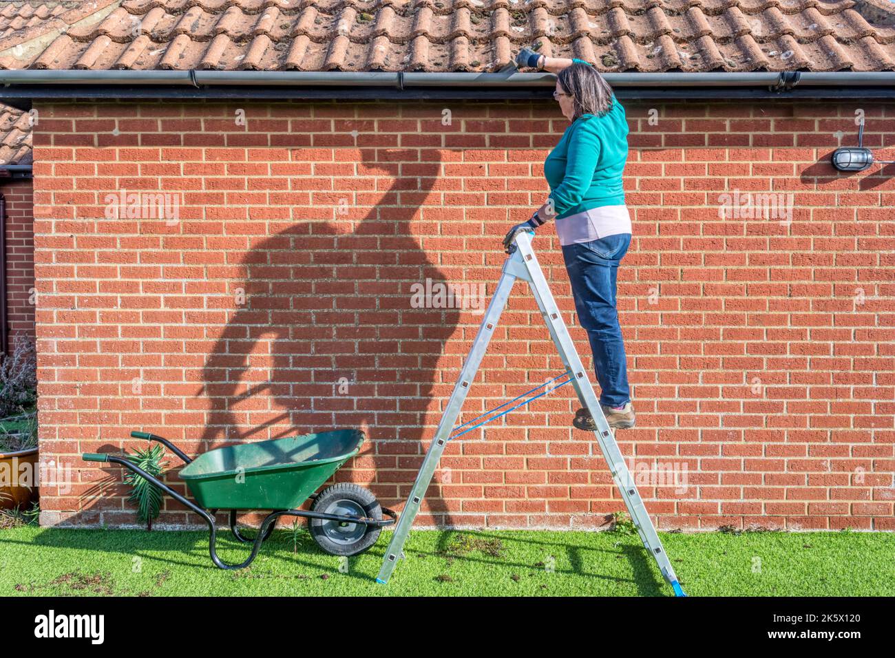 Woman clearing moss out of gutters to stop rain overflowing & running ...