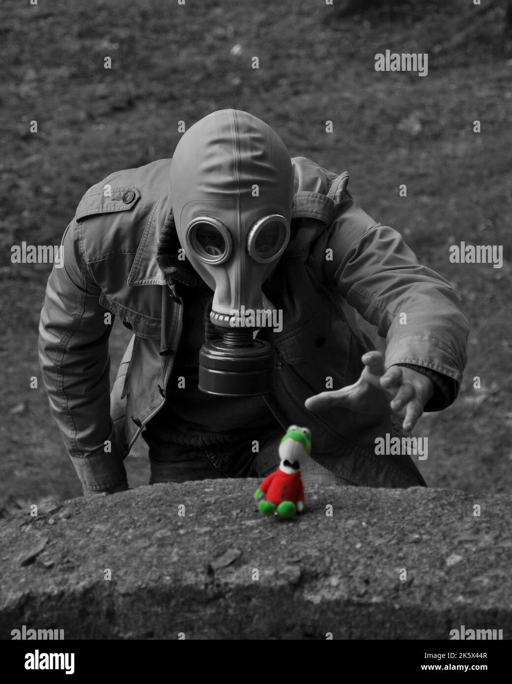 A grayscale of a male in a gas mask reaching to a toy Stock Photo - Alamy