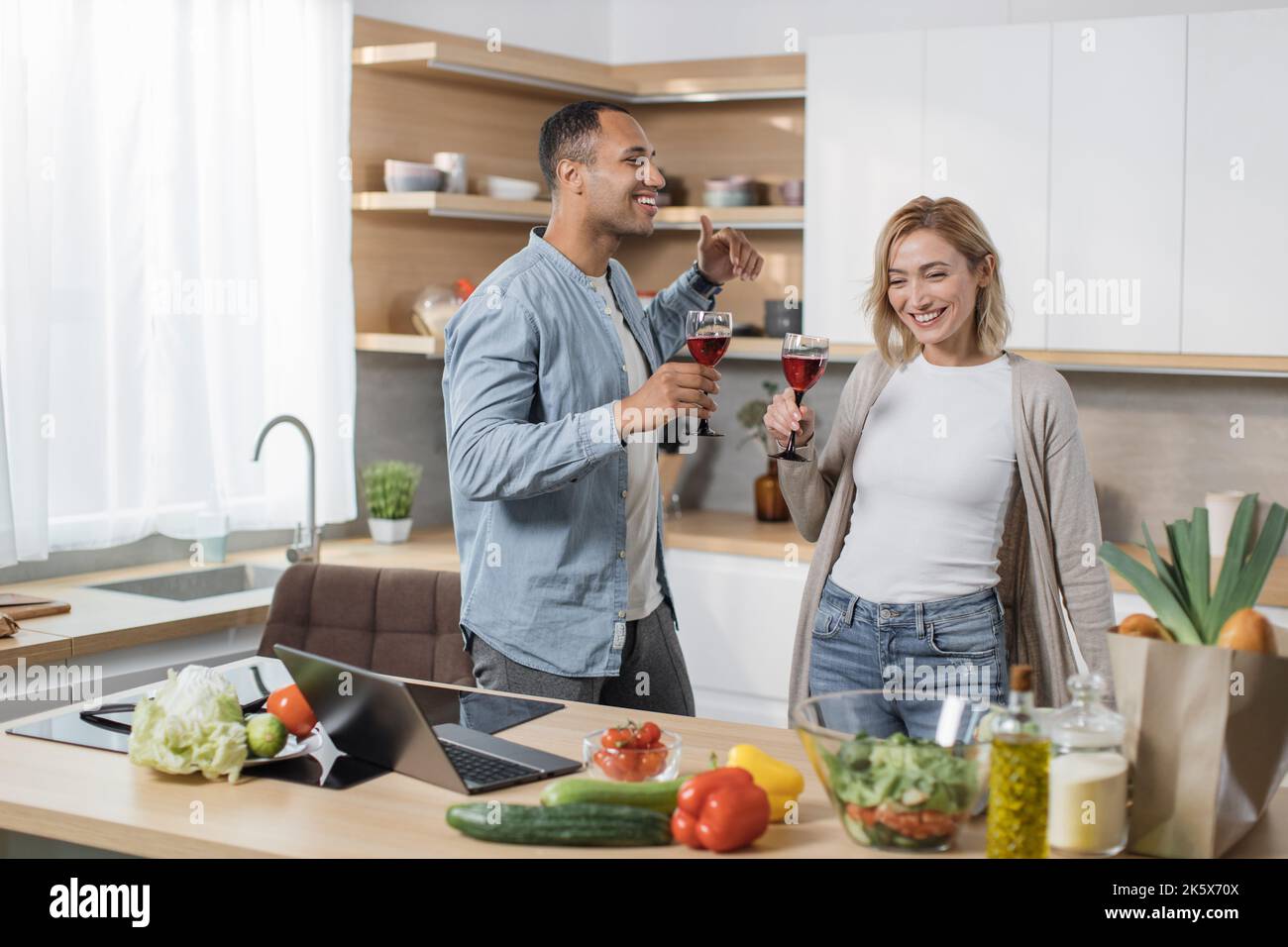 Happy multinational couple having fun while cooking healthy vegetarian ...