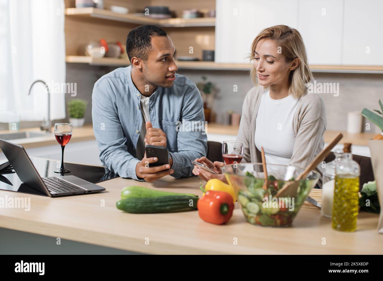 Happy multinational couple using cell phone while having breakfast at ...