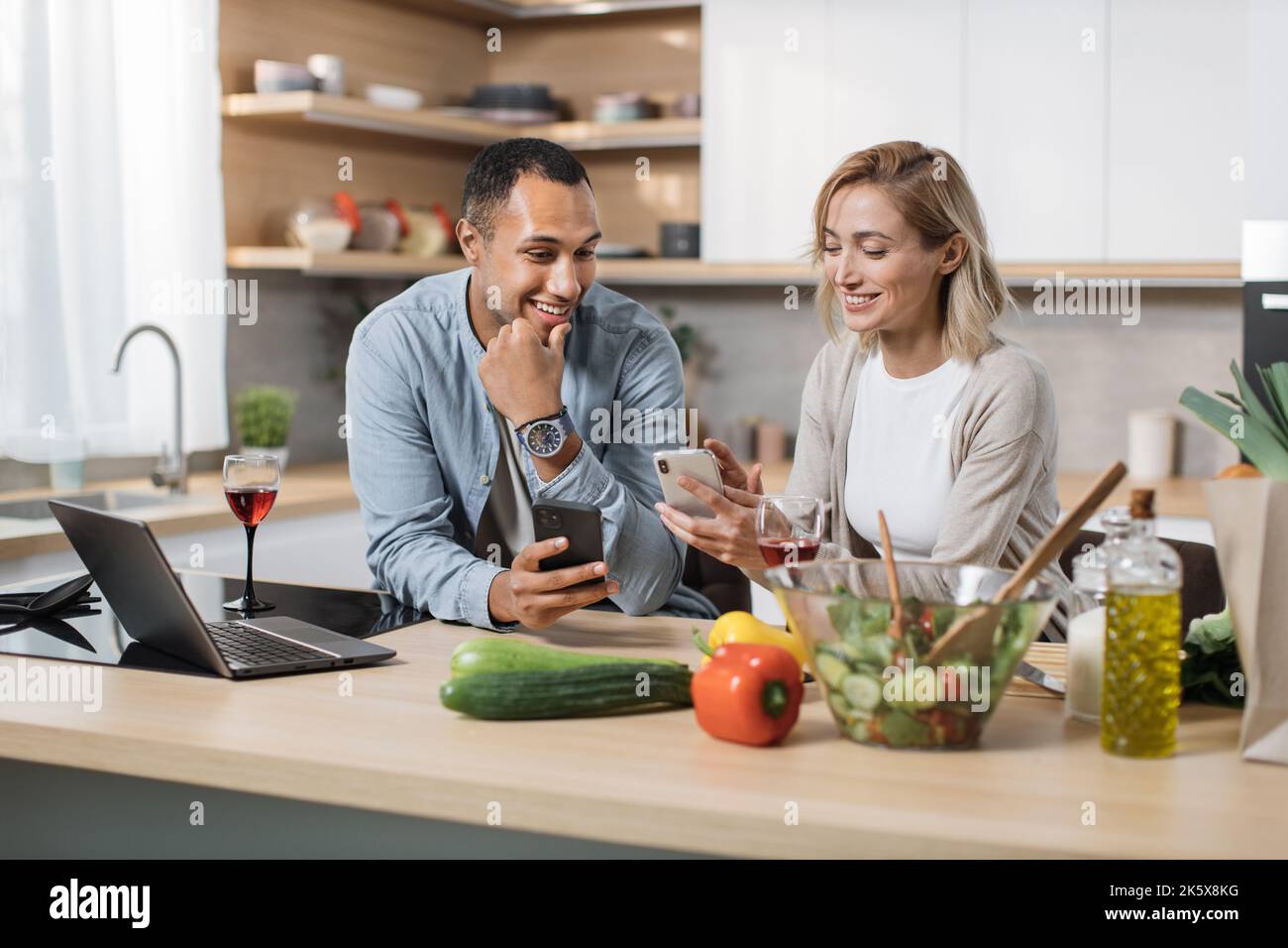 Happy multinational couple using cell phone while having breakfast at ...