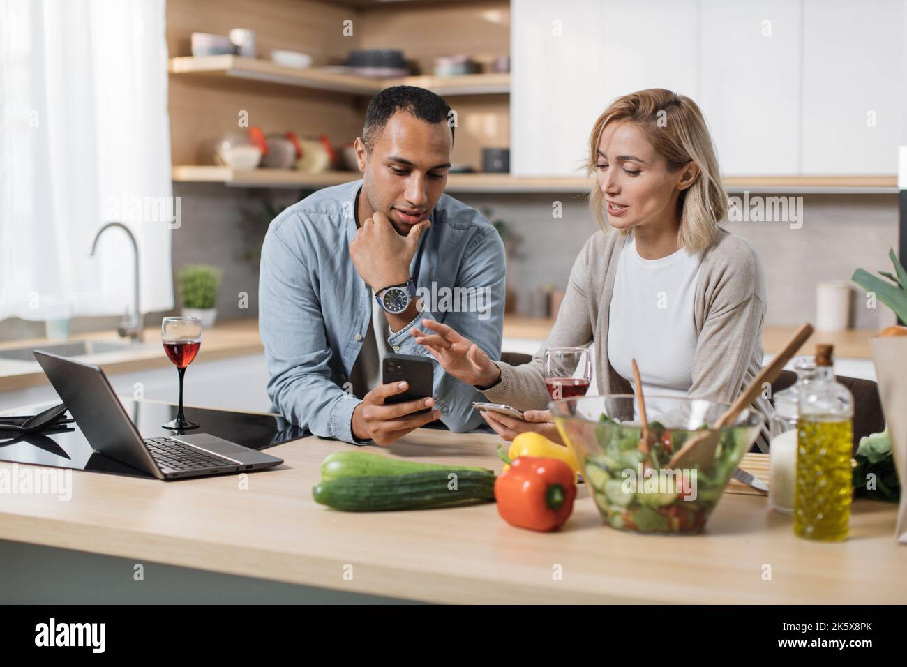 Happy multinational couple using cell phone while having breakfast at ...