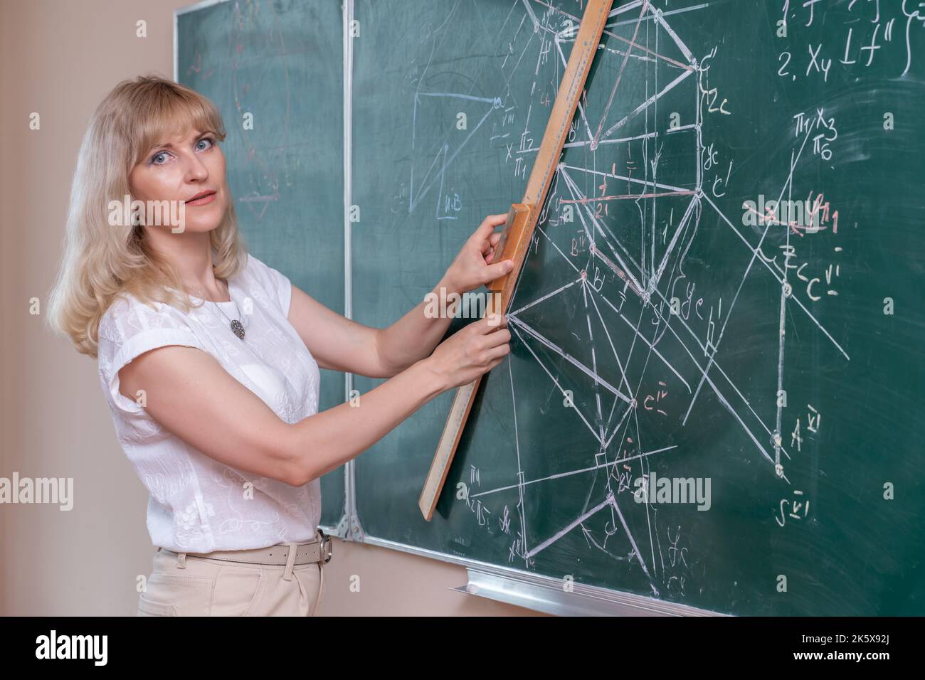 A young Caucasian female math teacher stands at the blackboard and ...