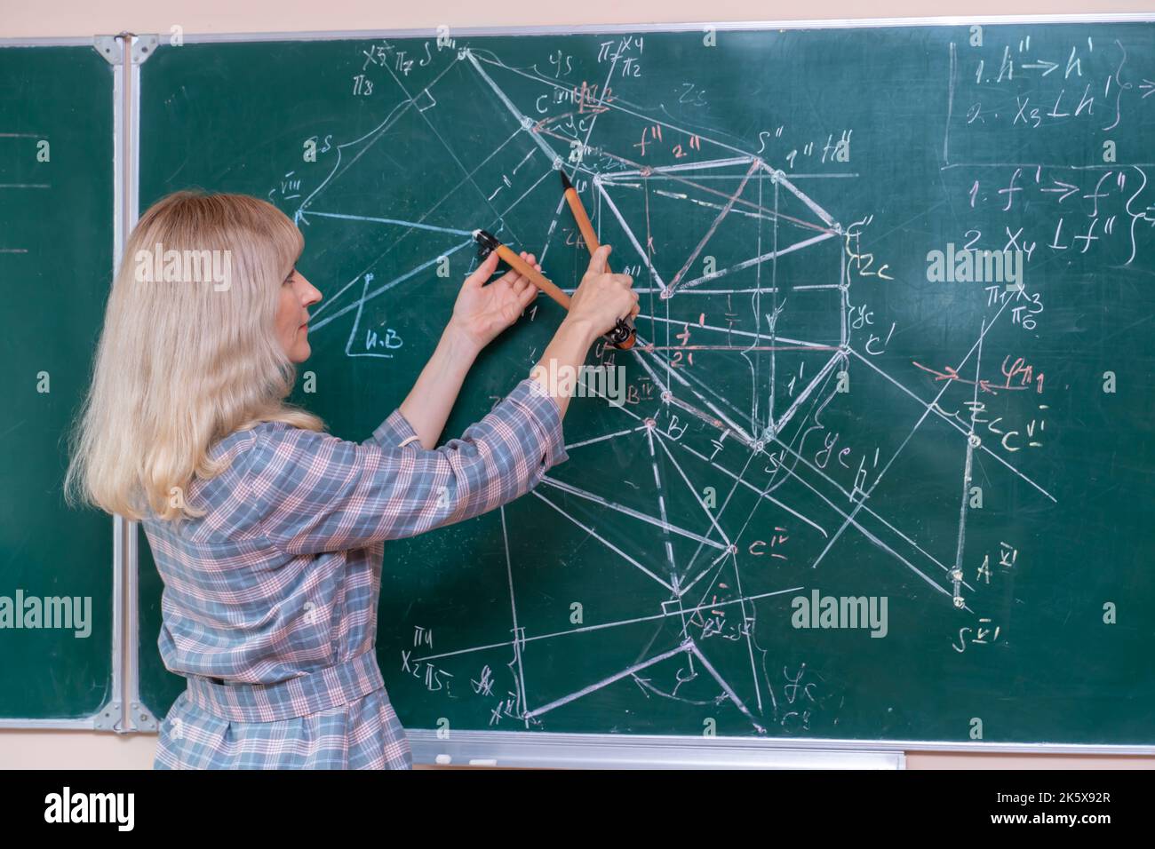 A young Caucasian female math teacher stands at the blackboard and ...