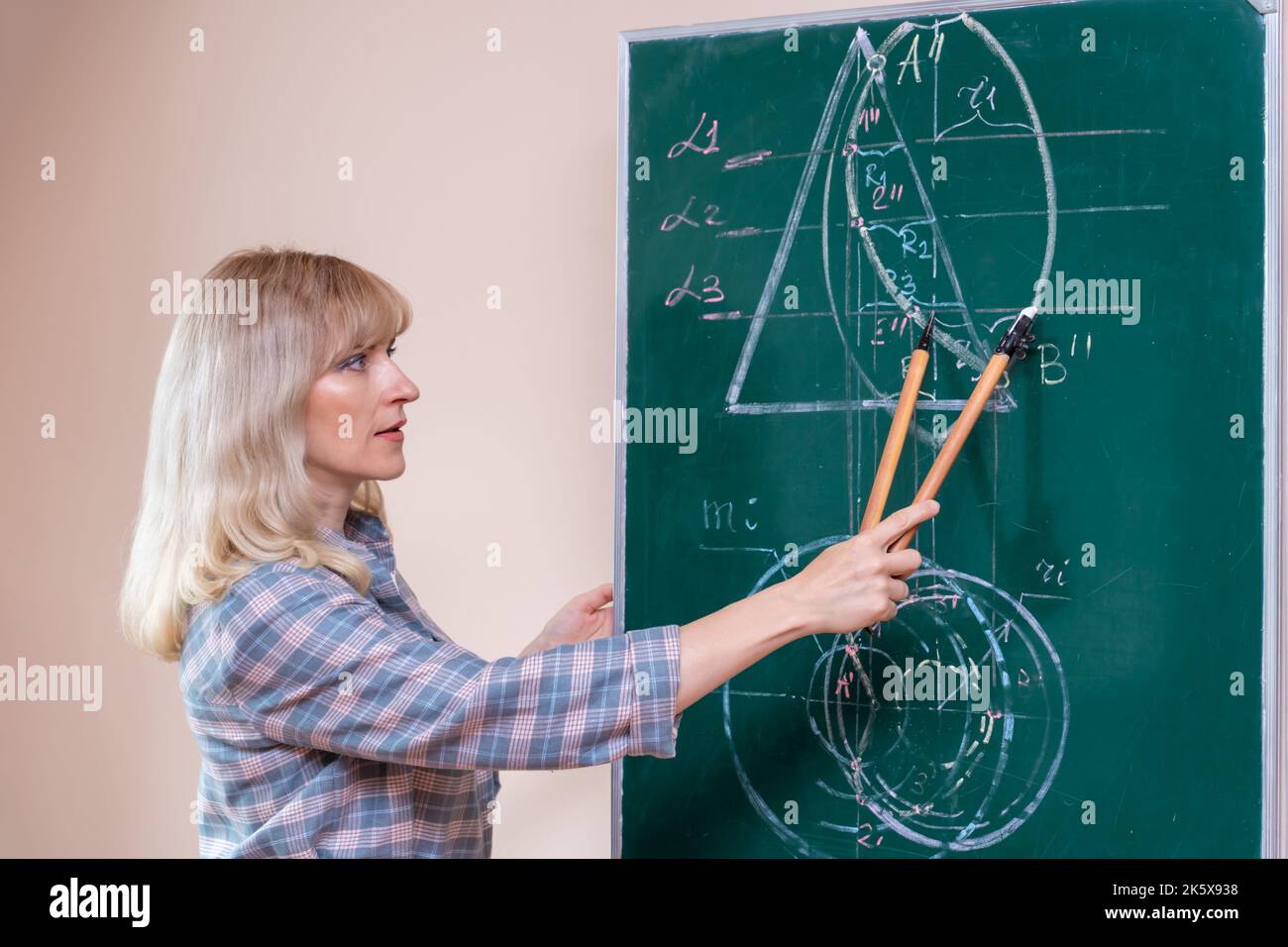 A young Caucasian female math teacher stands at the blackboard and ...
