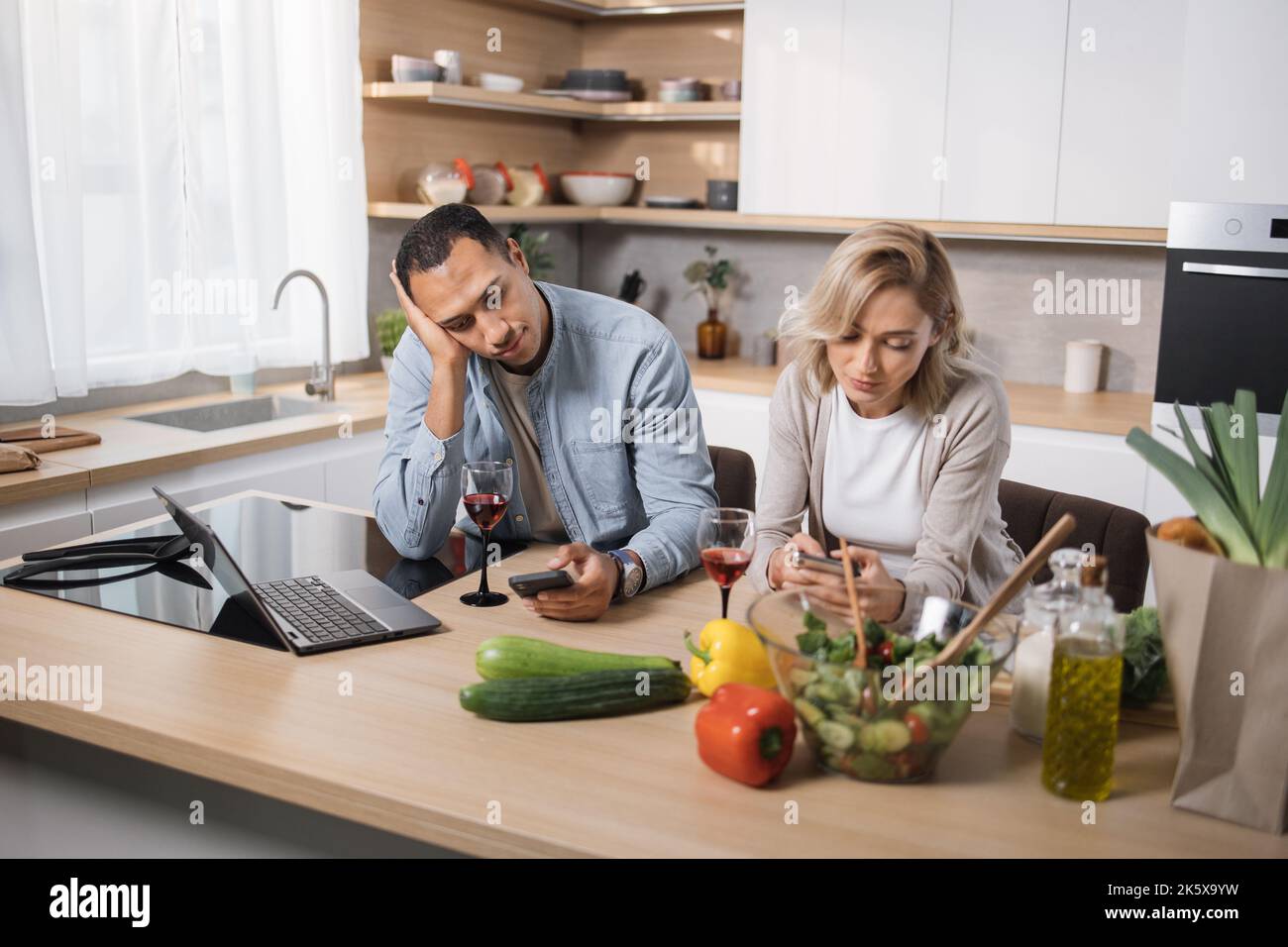 Tired, emotionless multinational couple eating salad using smartphone ...