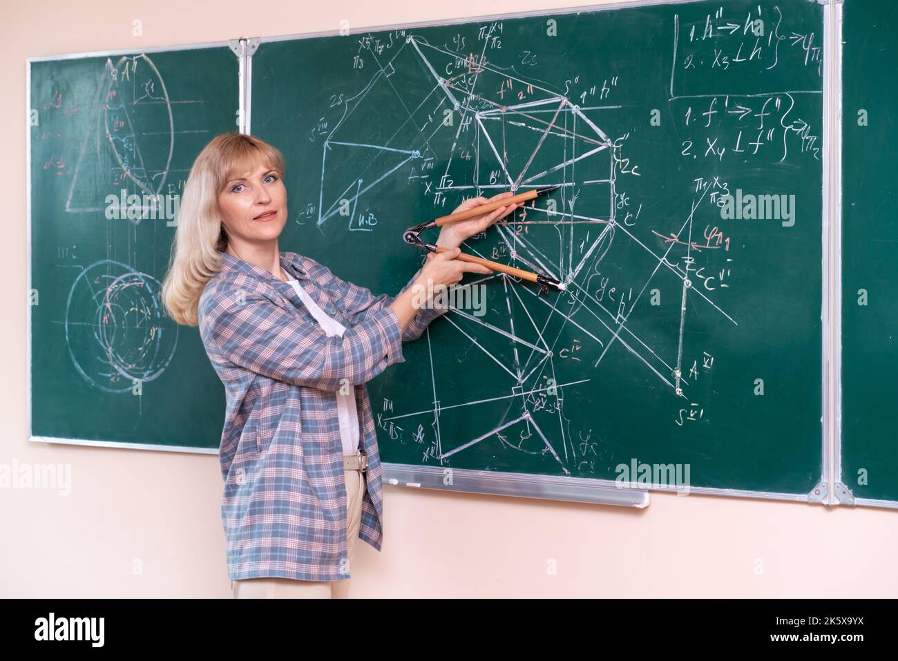 A young Caucasian female math teacher stands at the blackboard and ...