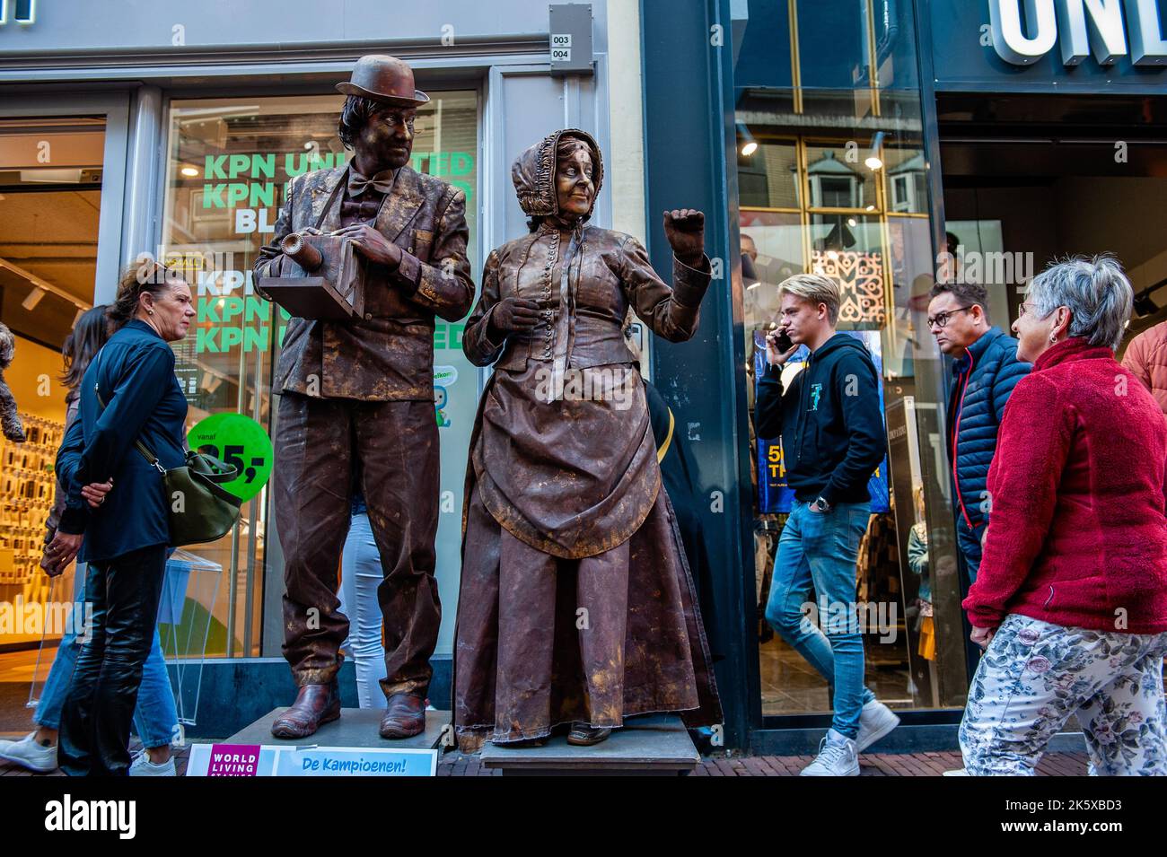 People are seen passing by behind of a couple performing as living ...