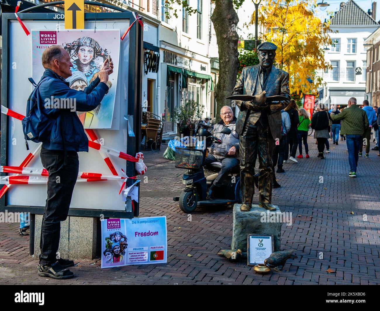 A man takes a photo of a performing living statue with his mobile phone ...