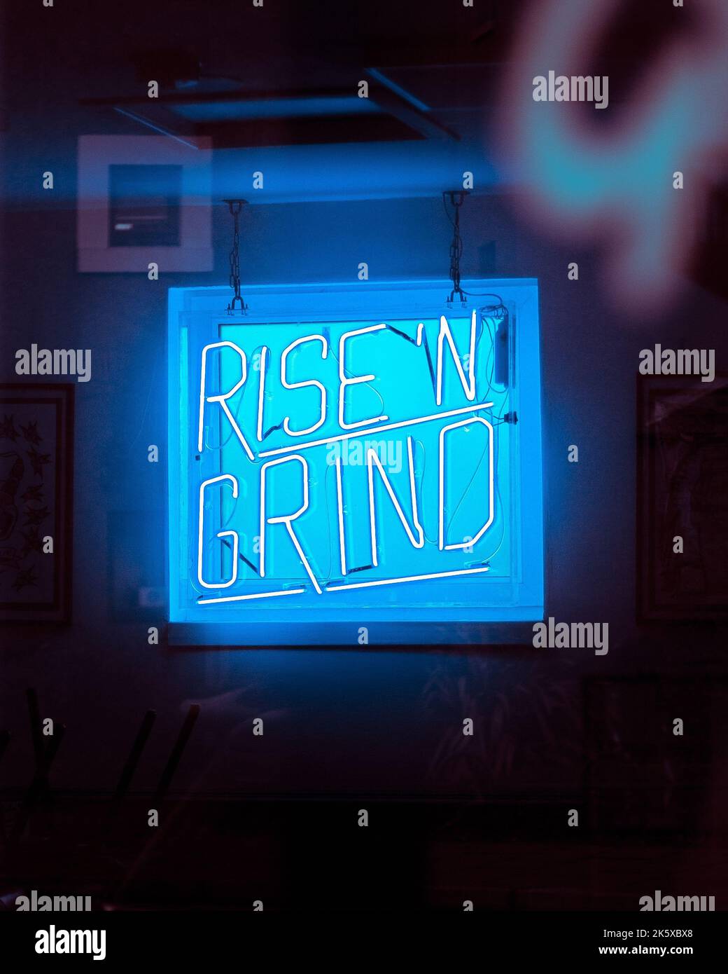 A vertical of a neon blue "Rise 'N Grind" sign in a dark room Stock ...