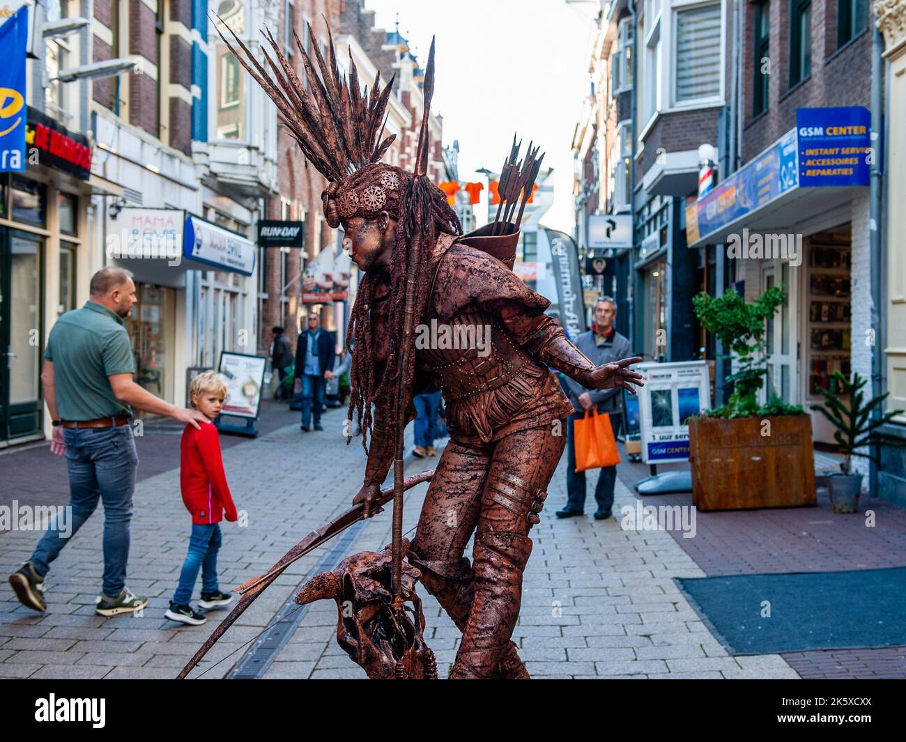 People along the street watch one of the living statues performing ...