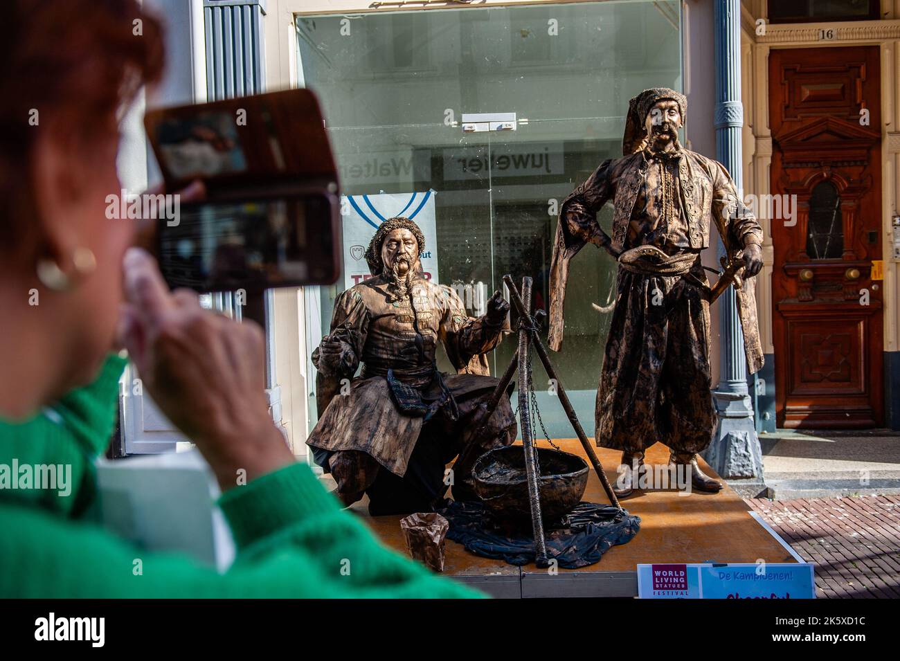 A woman is seen taking a photo of two artists performing as living ...