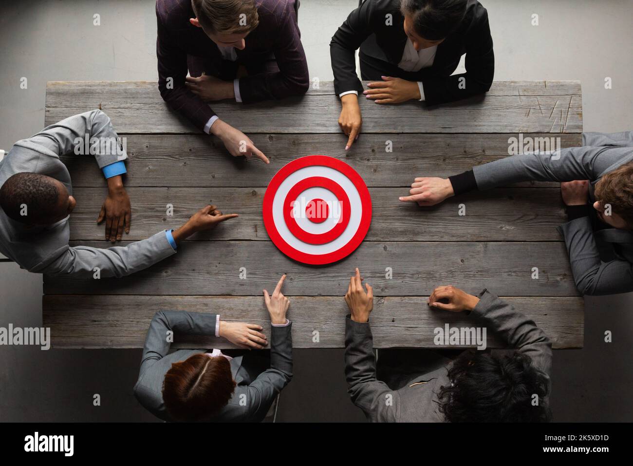 Team of business people pointing at red target at meeting table ...
