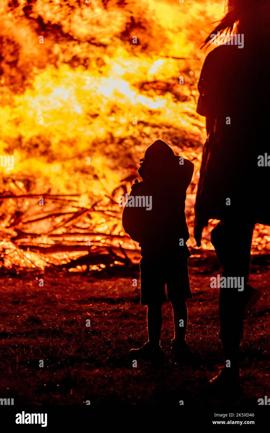 A vertical shot of a fire flaring up and a child and an adult looking ...