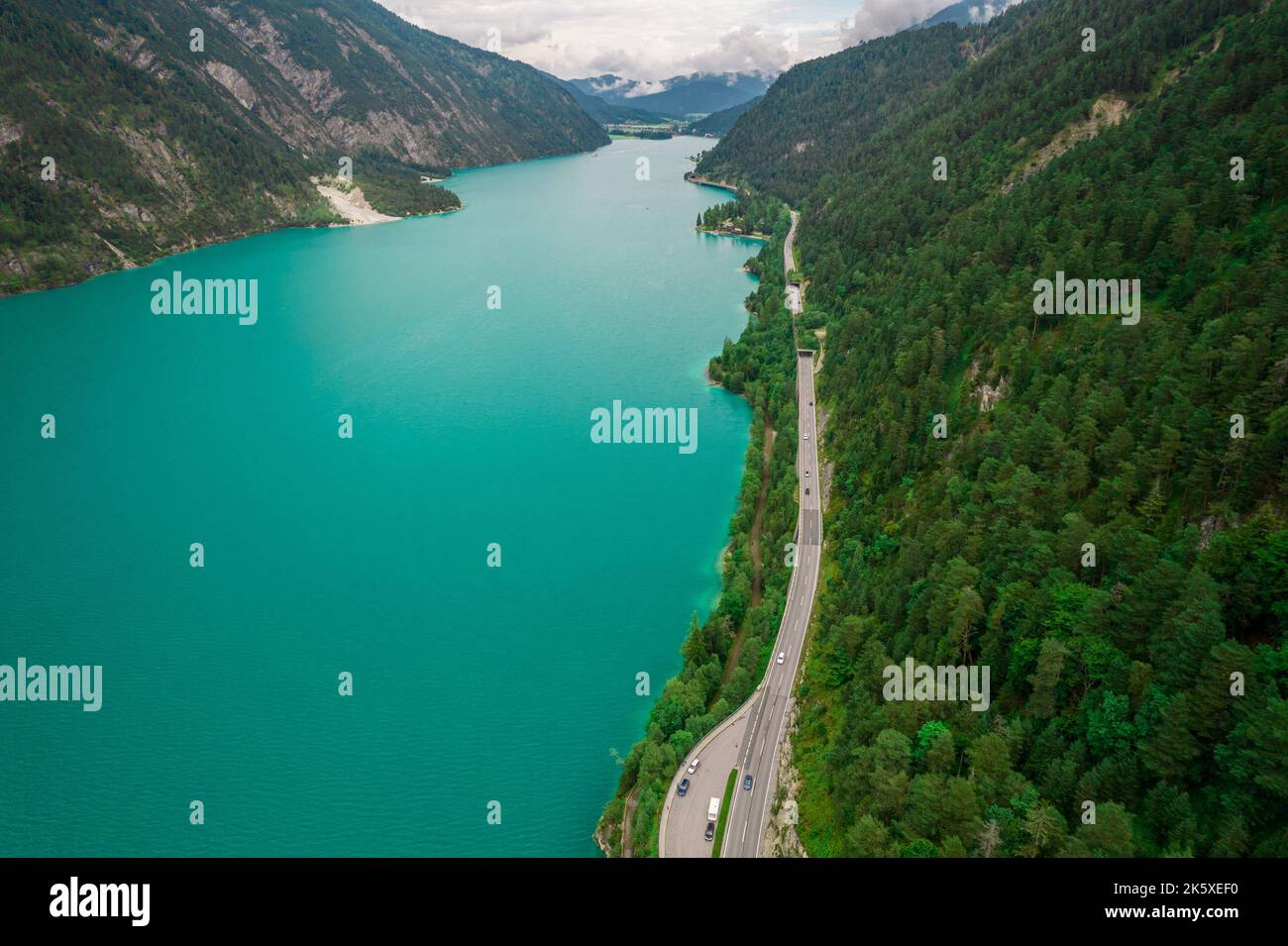An aerial view of a road by Achen Lake between lush green steep ...