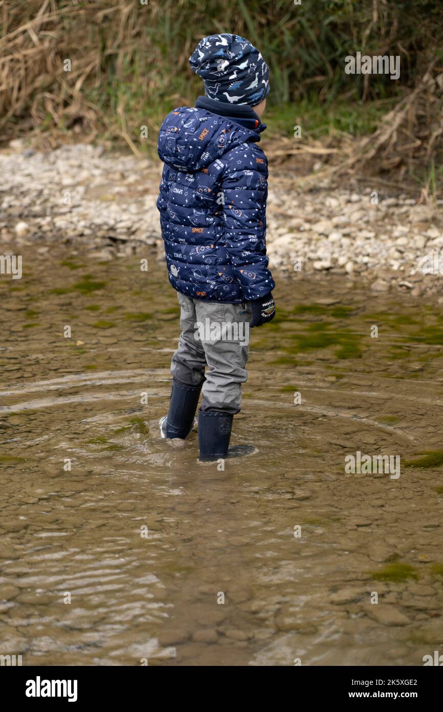 little boy stands on the bank of river, admires the magnificent view of ...