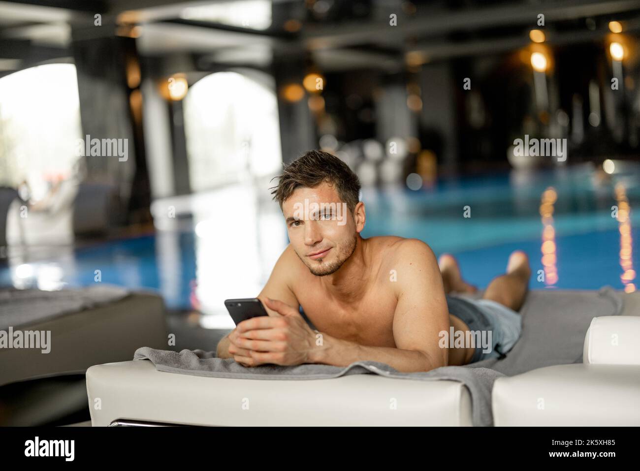 Man rests with phone by the swimming pool indoors at spa resort Stock ...