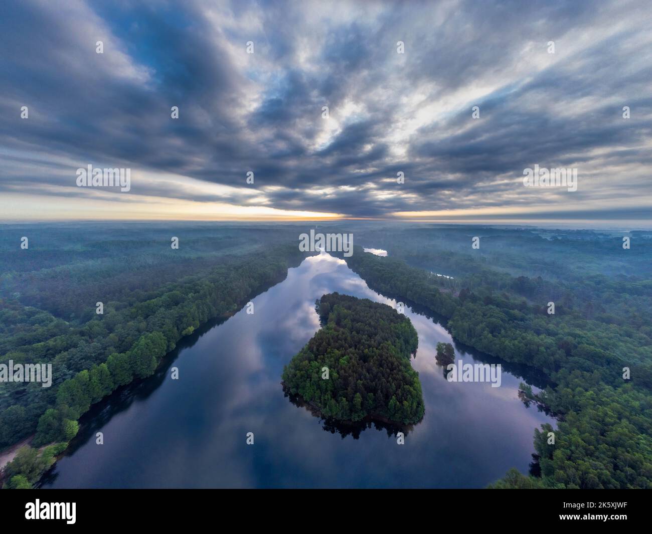 A bird's-eye shot of a forest island in calm water reflecting the ...