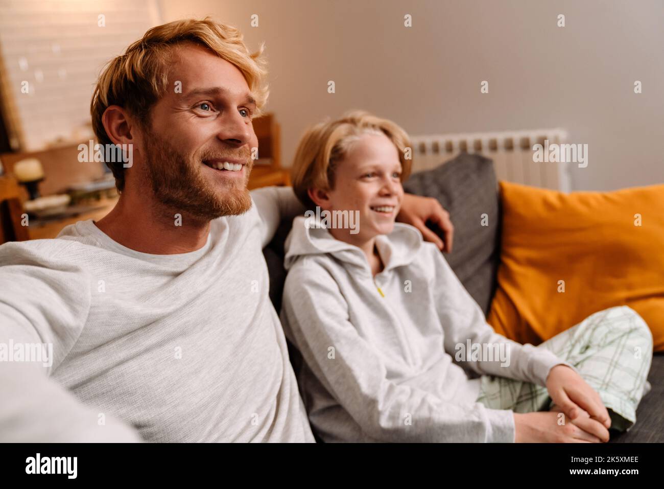 Ginger father and son laughing together while resting on couch at home ...