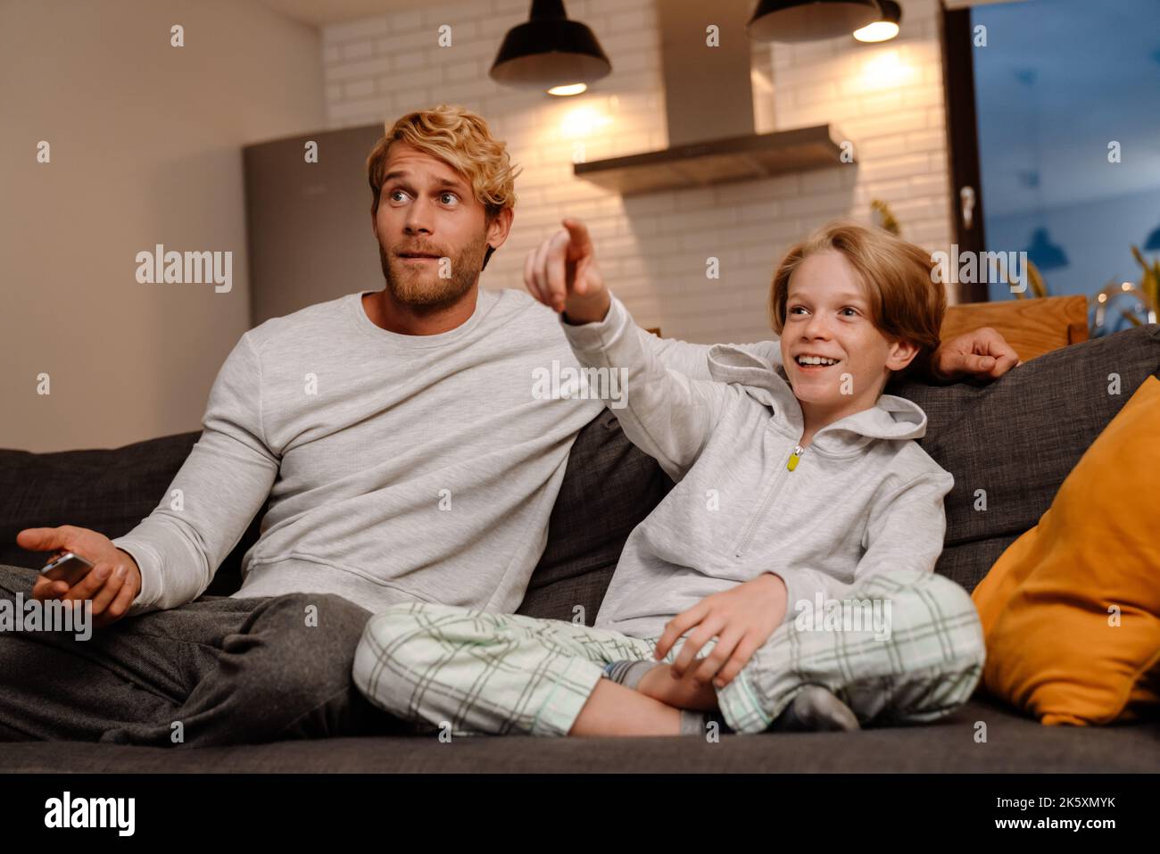Ginger father and son smiling and watching tv while resting on couch at ...