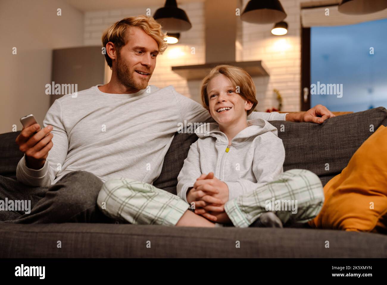Ginger father and son smiling and watching tv while resting on couch at ...