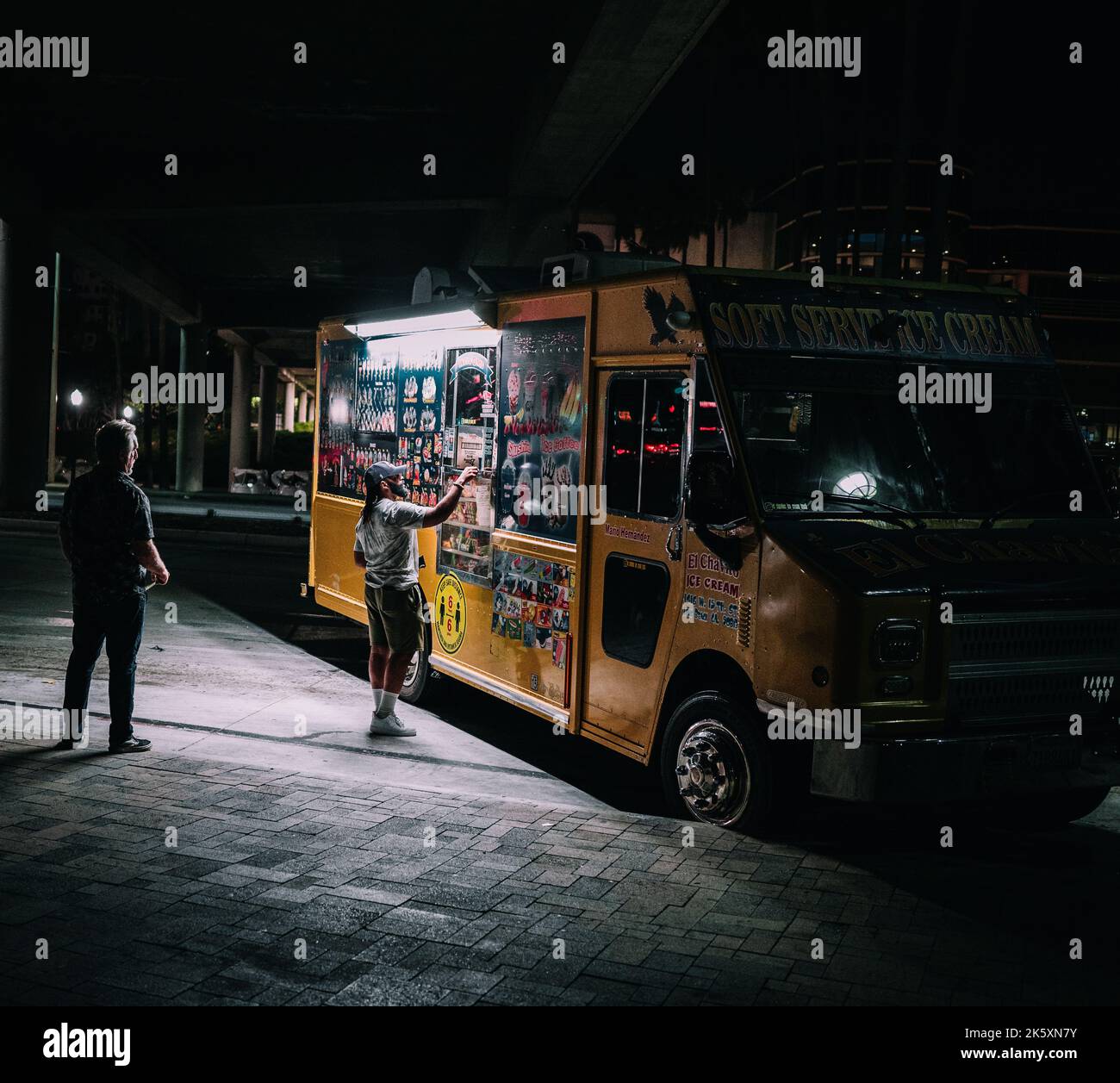 People line up outside a food service truck at night in Long BEach ...