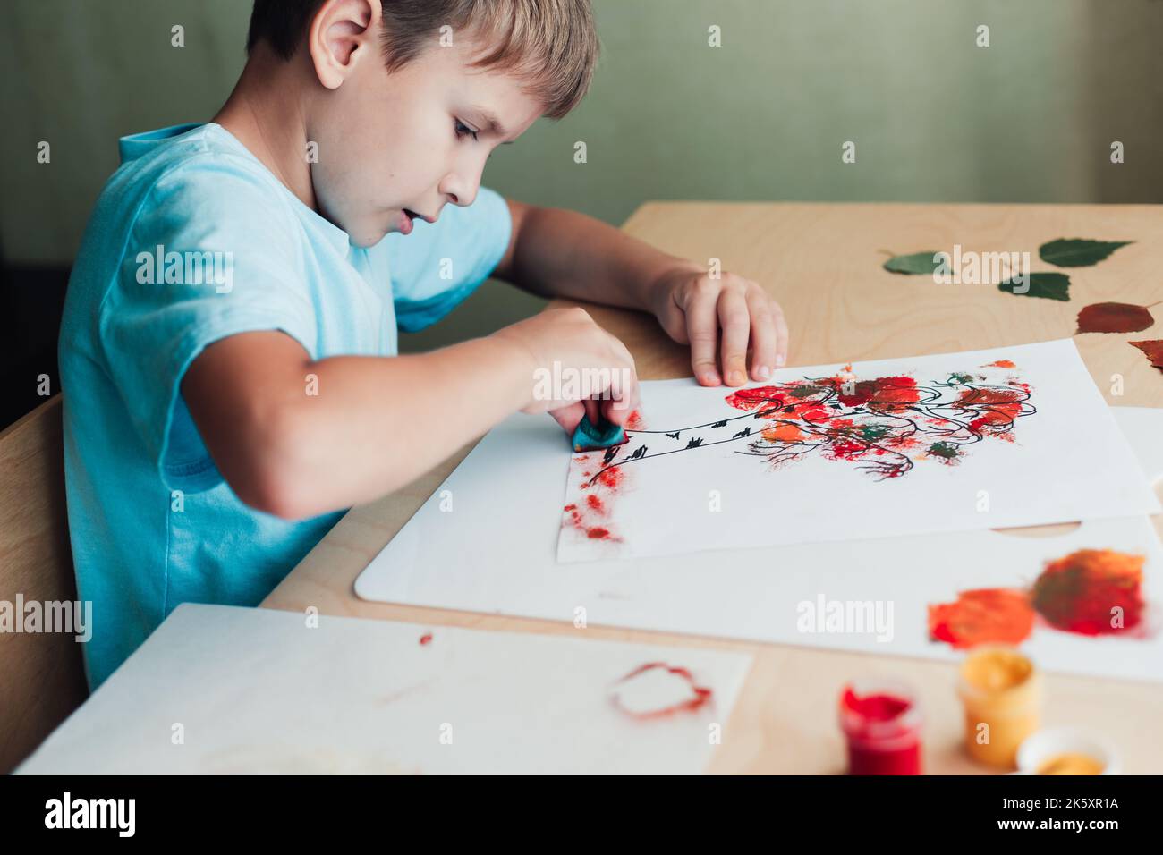 Cute child sitting at desk and making picture from colored dry birch ...